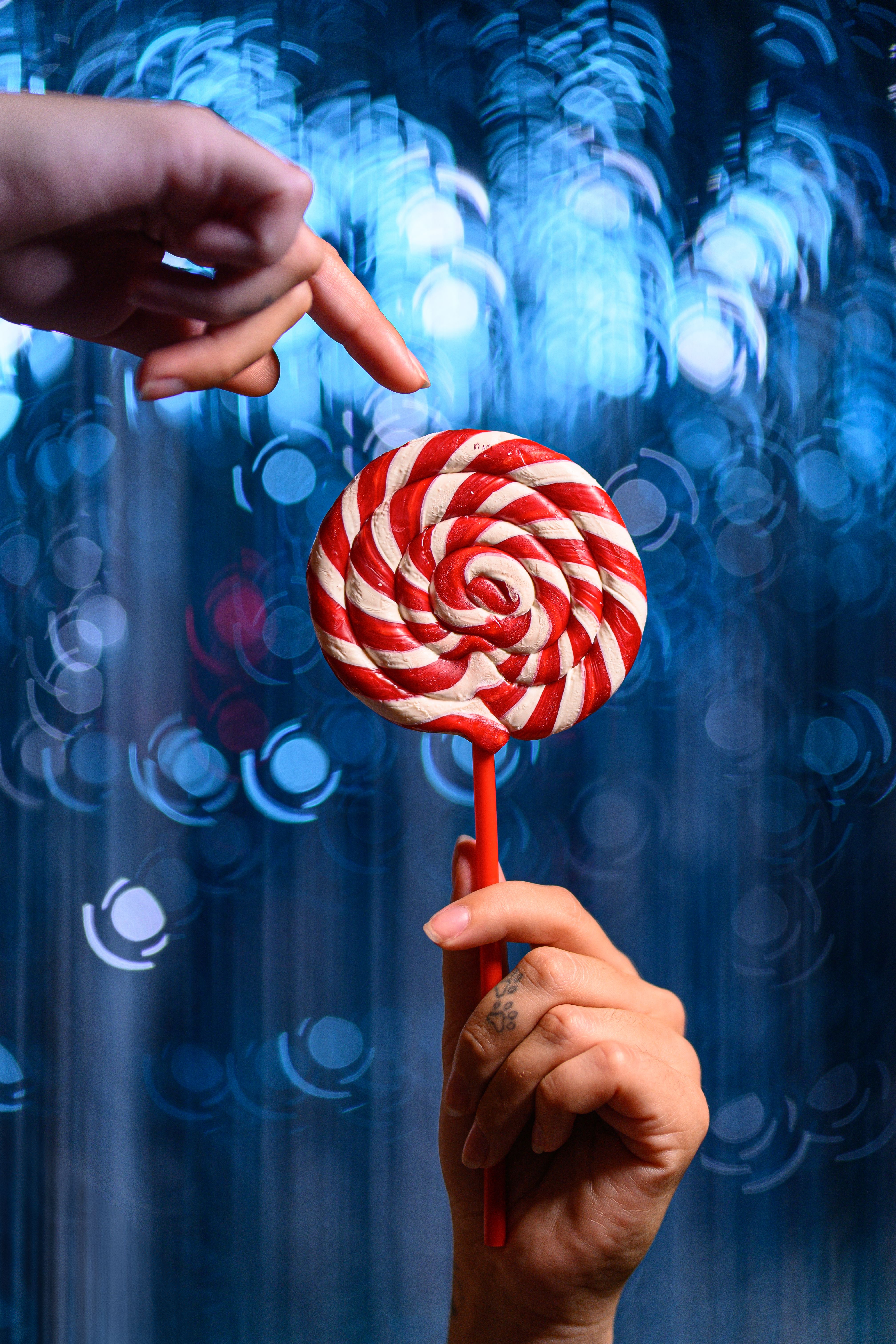 Hands Holding Swirled Red Lollipop with Bokeh · Free Stock Photo