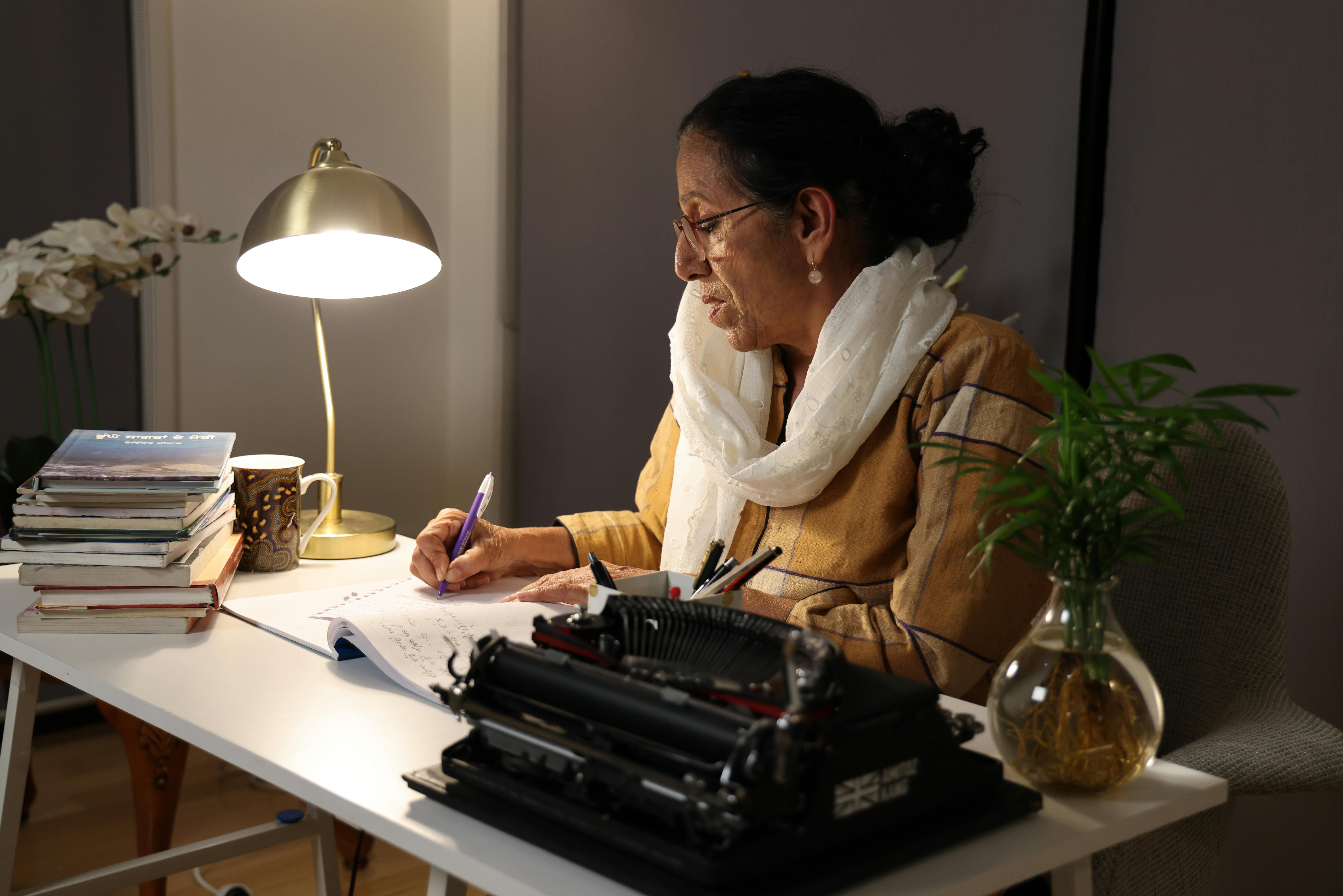 Mature Woman Writing at Desk with Typewriter · Free Stock Photo