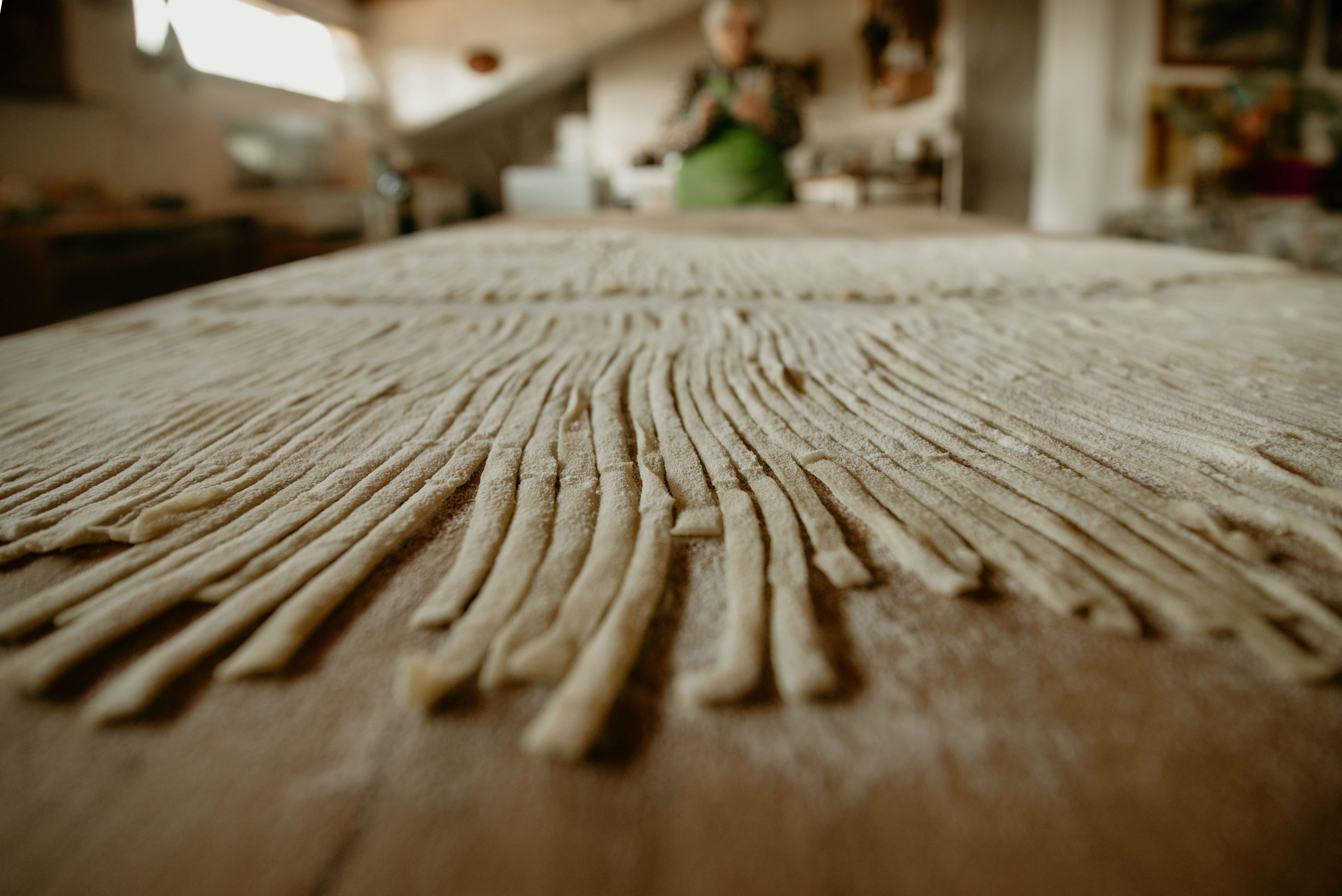Unrecognizable female rolling pasta dough on floury table at home ...