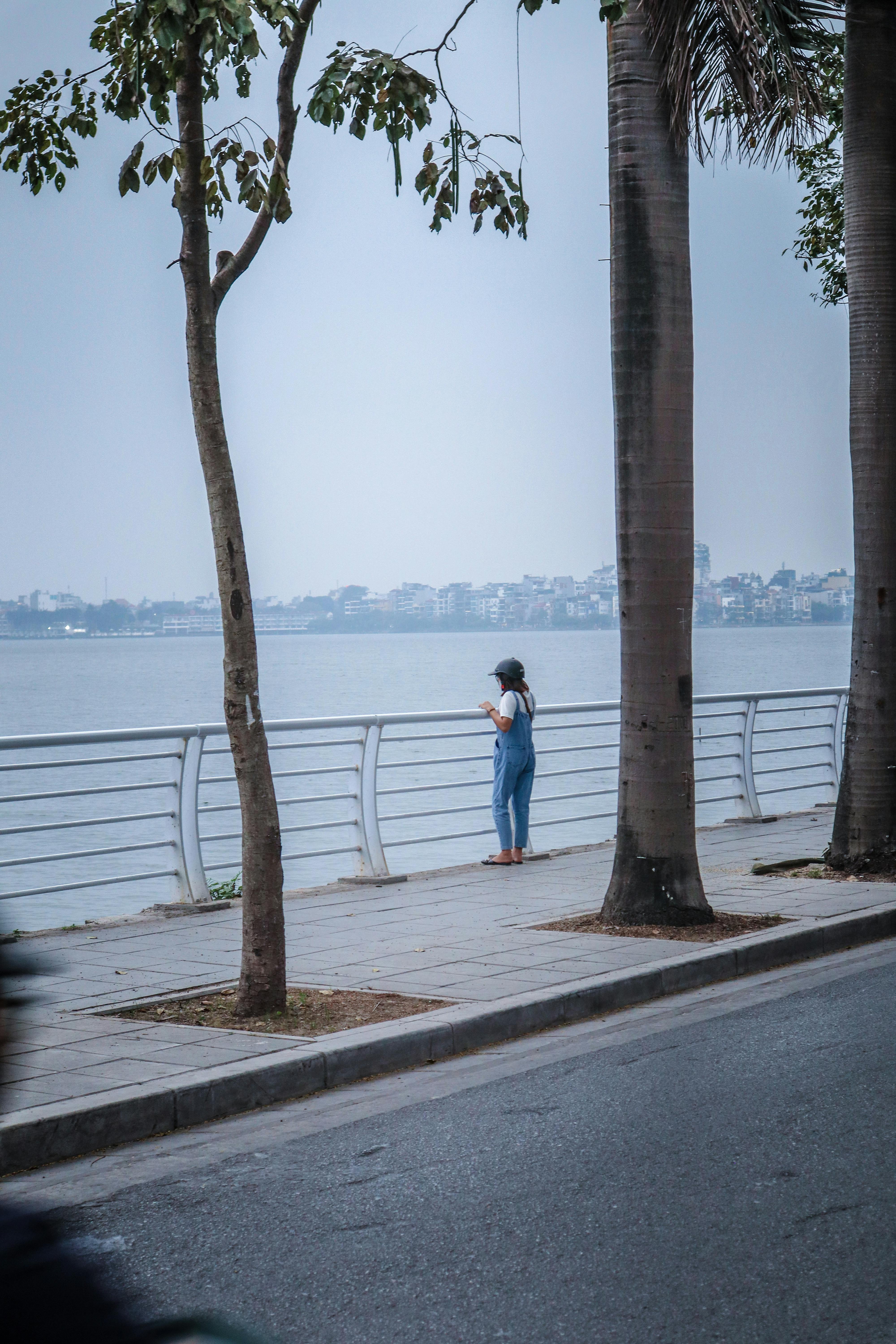 Woman Stands at Riverside Promenade in Casual Attire · Free Stock Photo