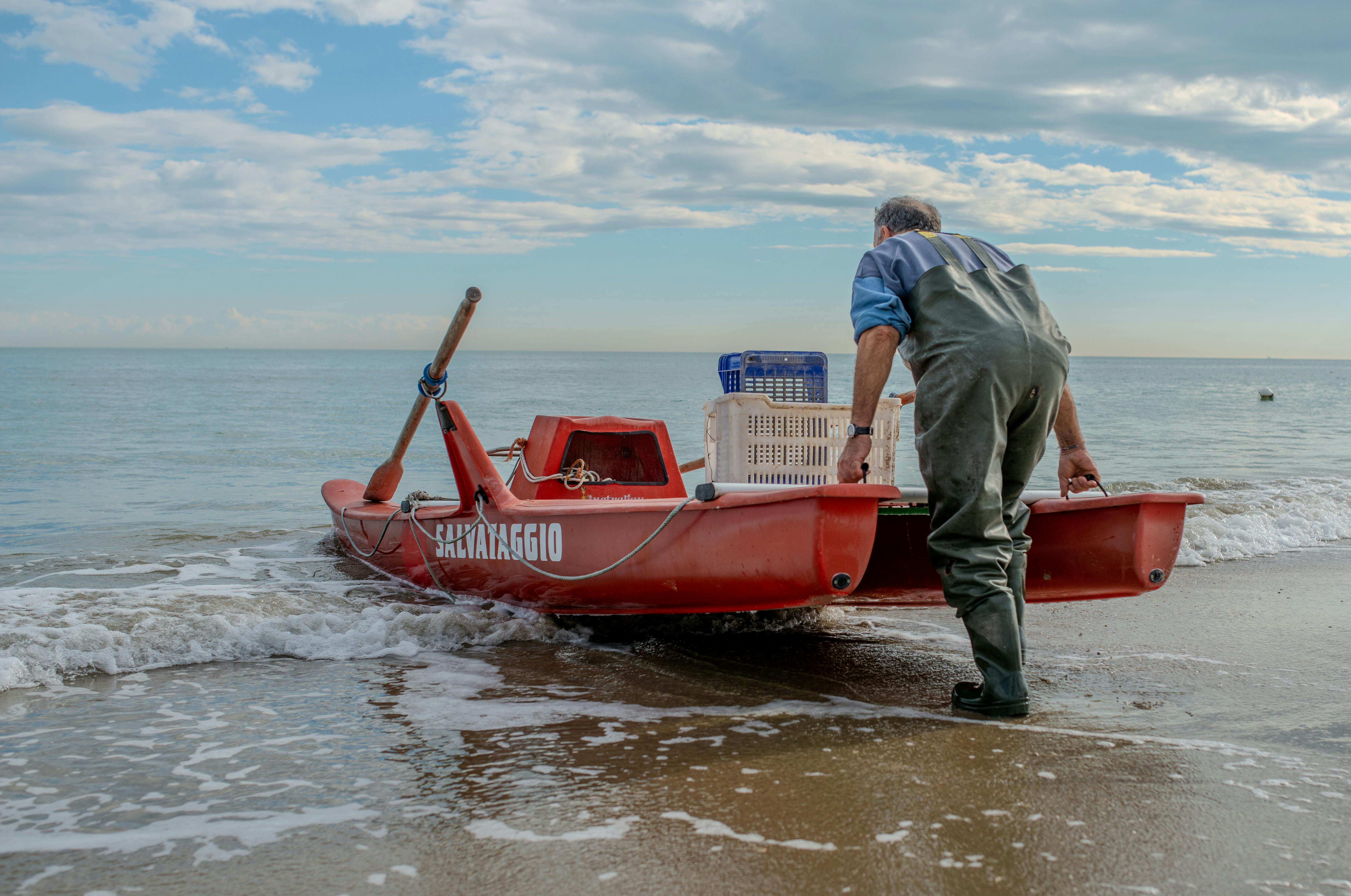 Man Pulling Red Lifeboat Ashore on Sandy Beach · Free Stock Photo