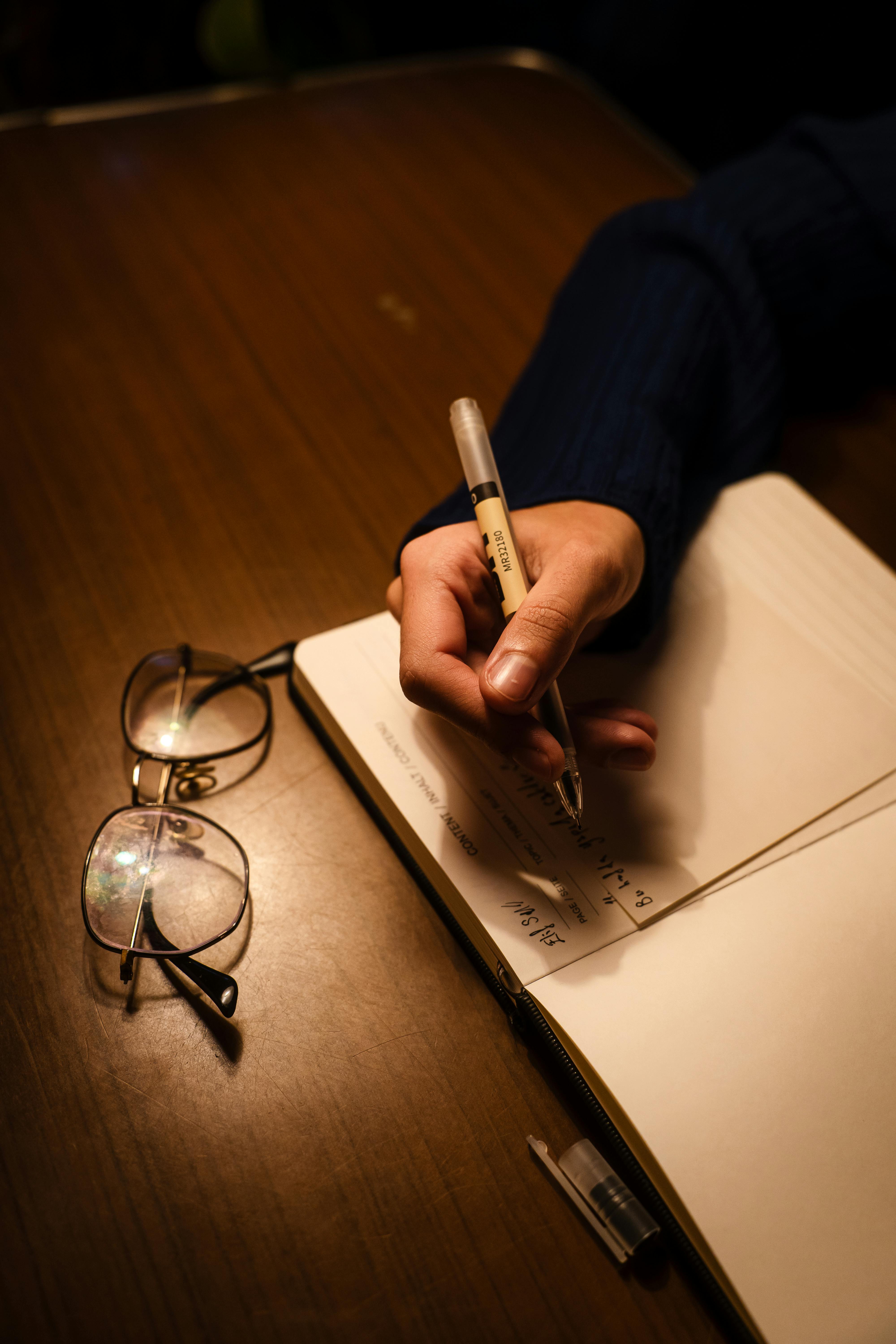 Person Writing in Journal with Pen and Glasses · Free Stock Photo