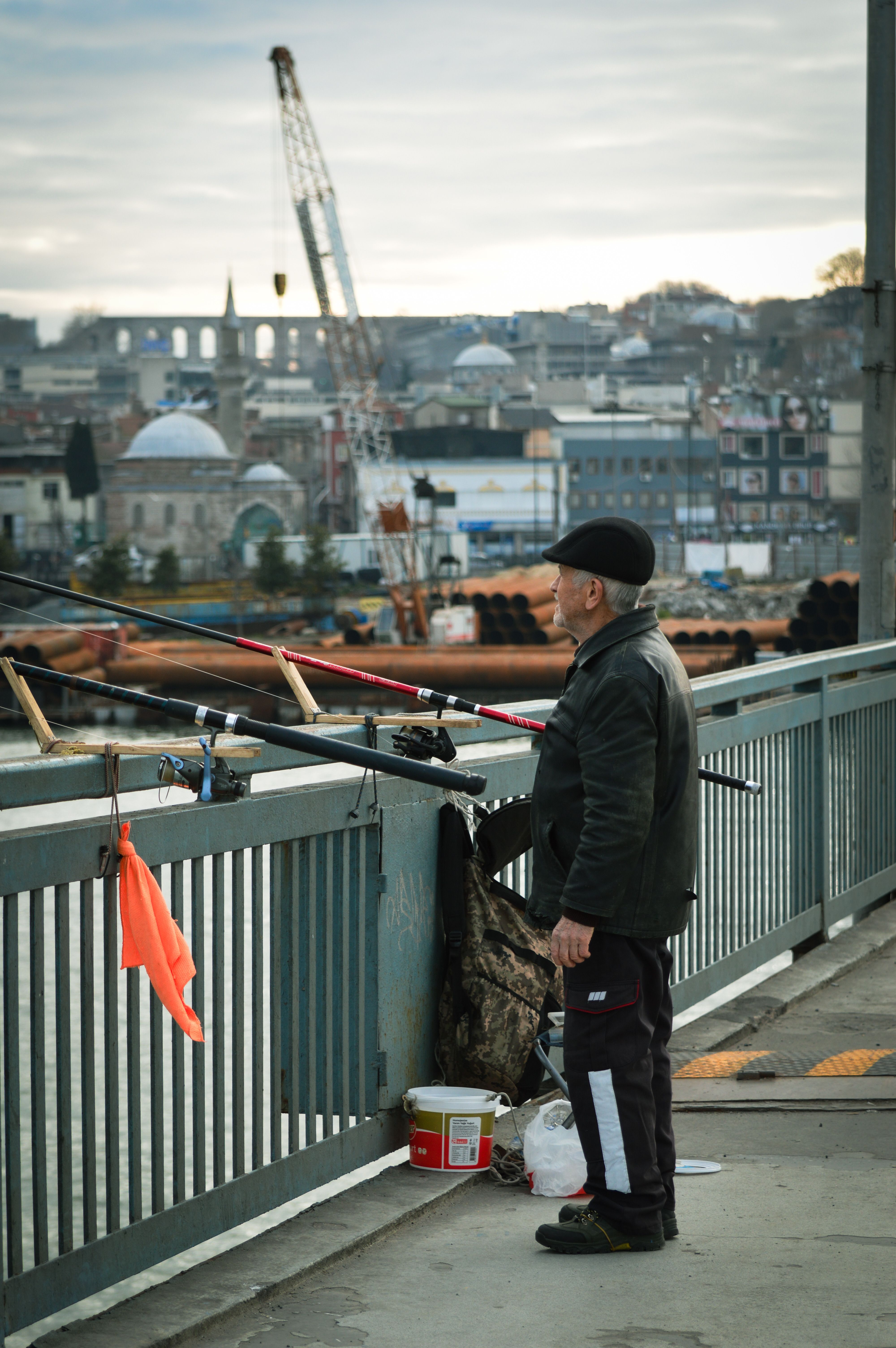 Man Fishing on Bridge Overlooking Urban Skyline · Free Stock Photo