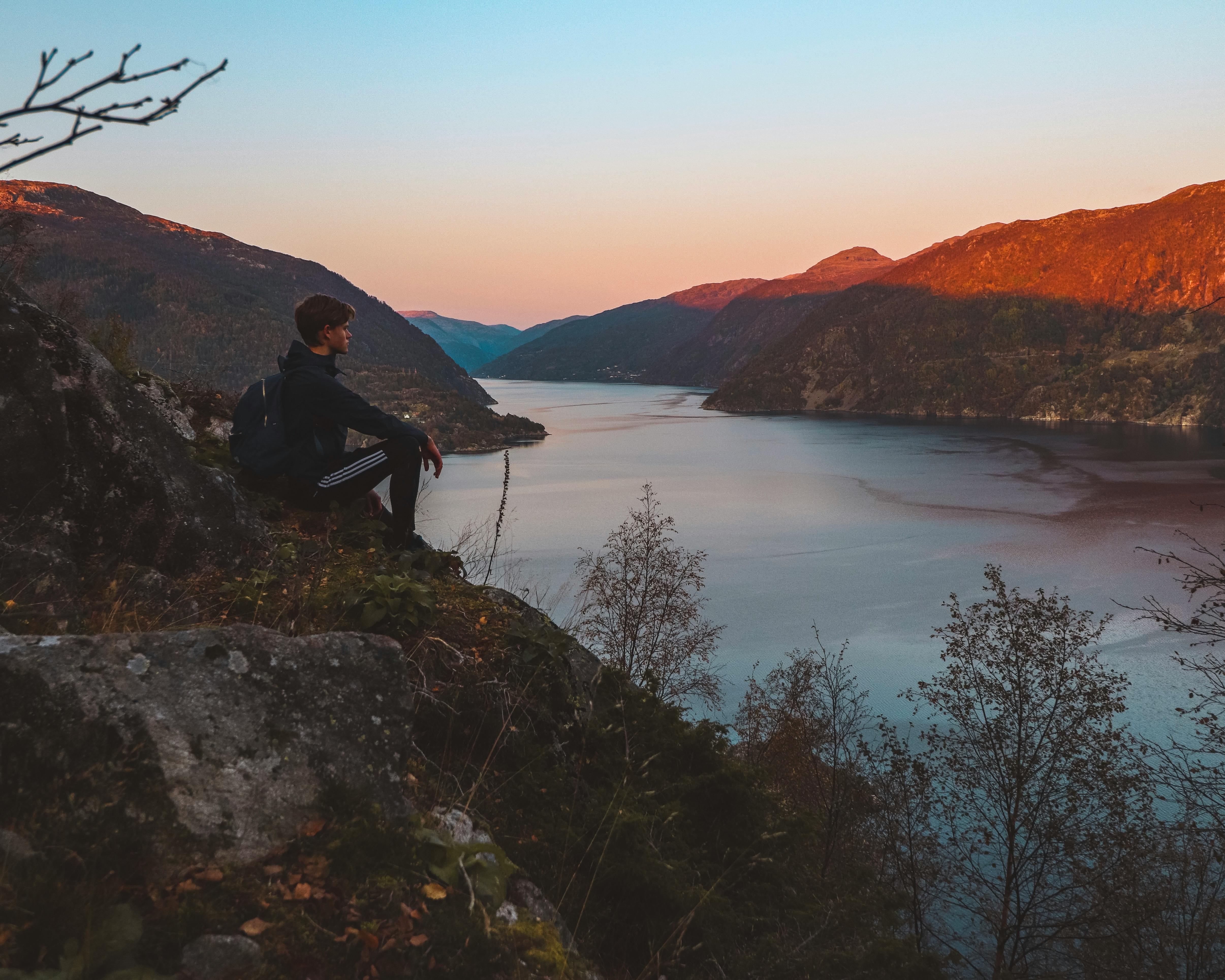 Man Sitting on Cliff Facing Calm Body of Water · Free Stock Photo