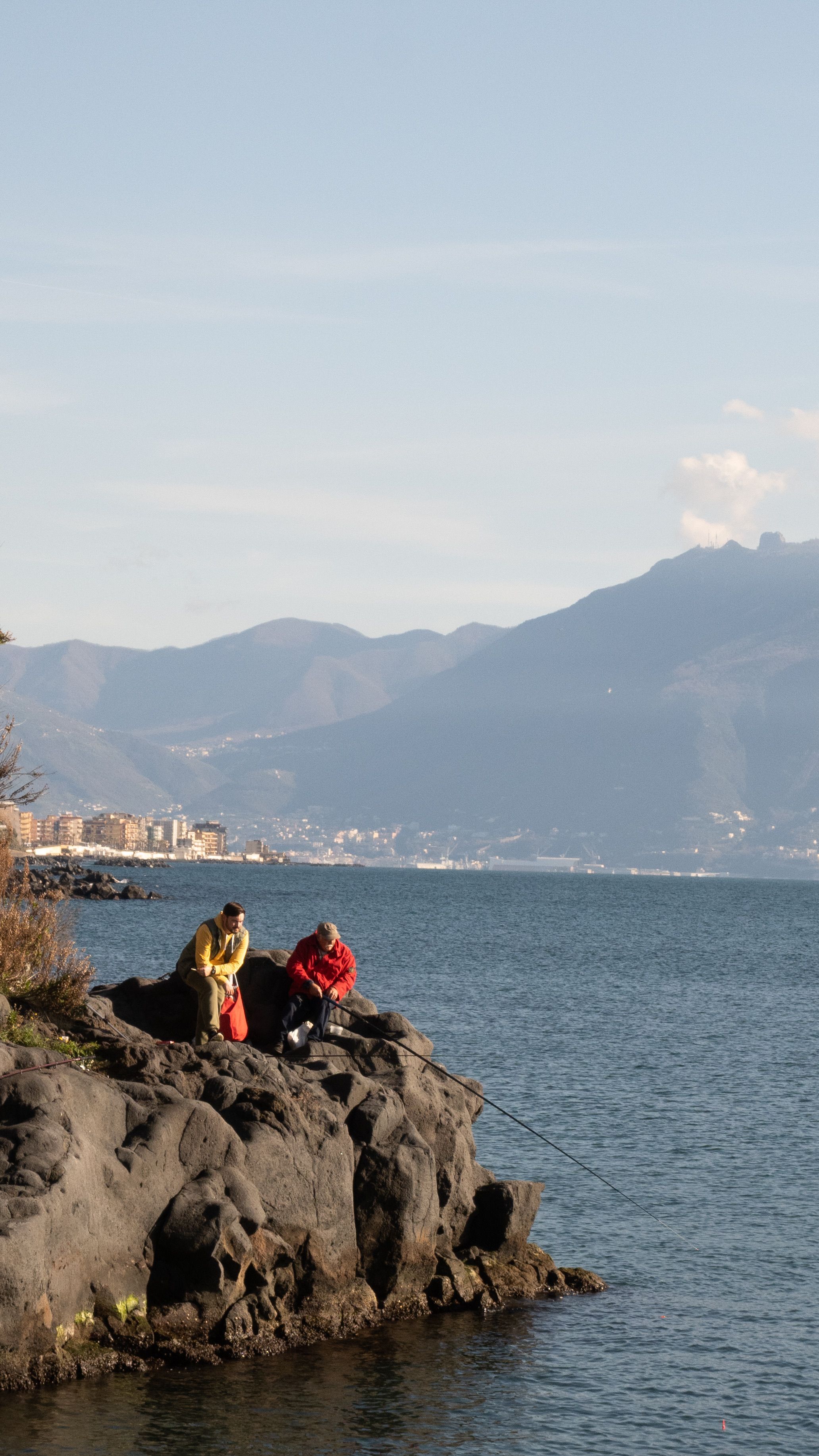 Two People Fishing on Rocky Shoreline with Mountain View · Free Stock Photo