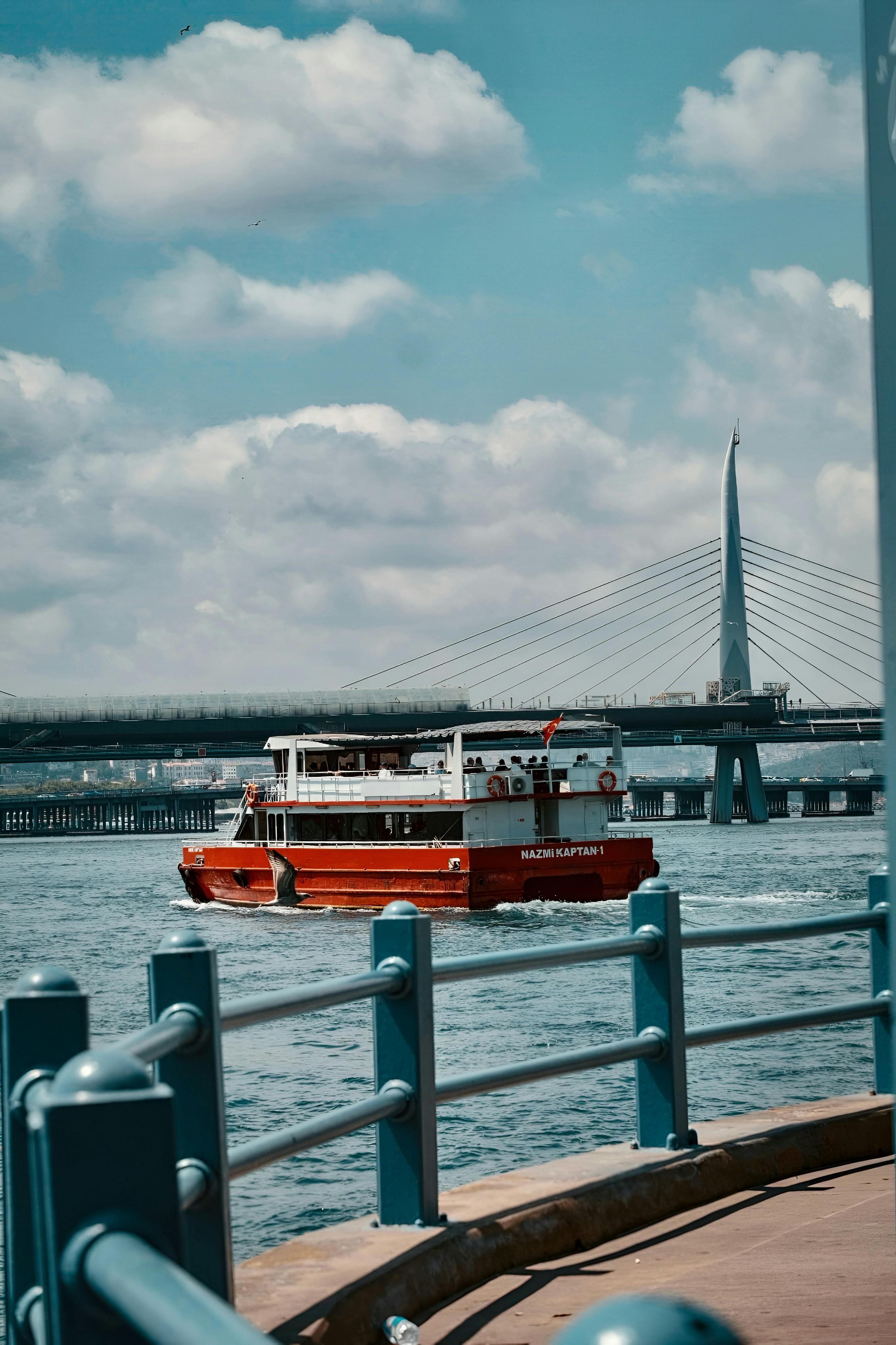 Red ferry boat cruising past modern suspension bridge · Free Stock Photo