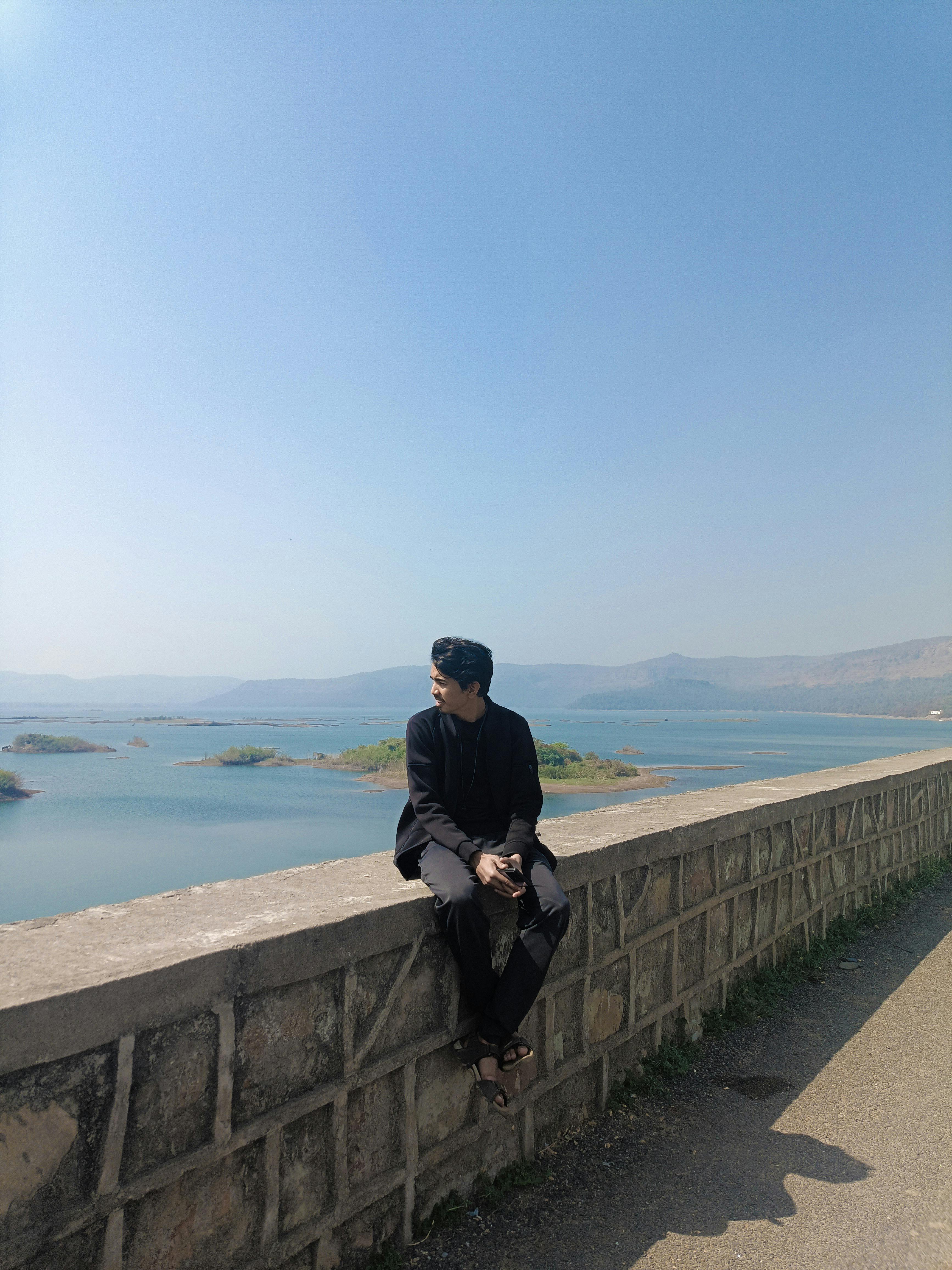 Man sitting on wall overlooking serene lake view · Free Stock Photo