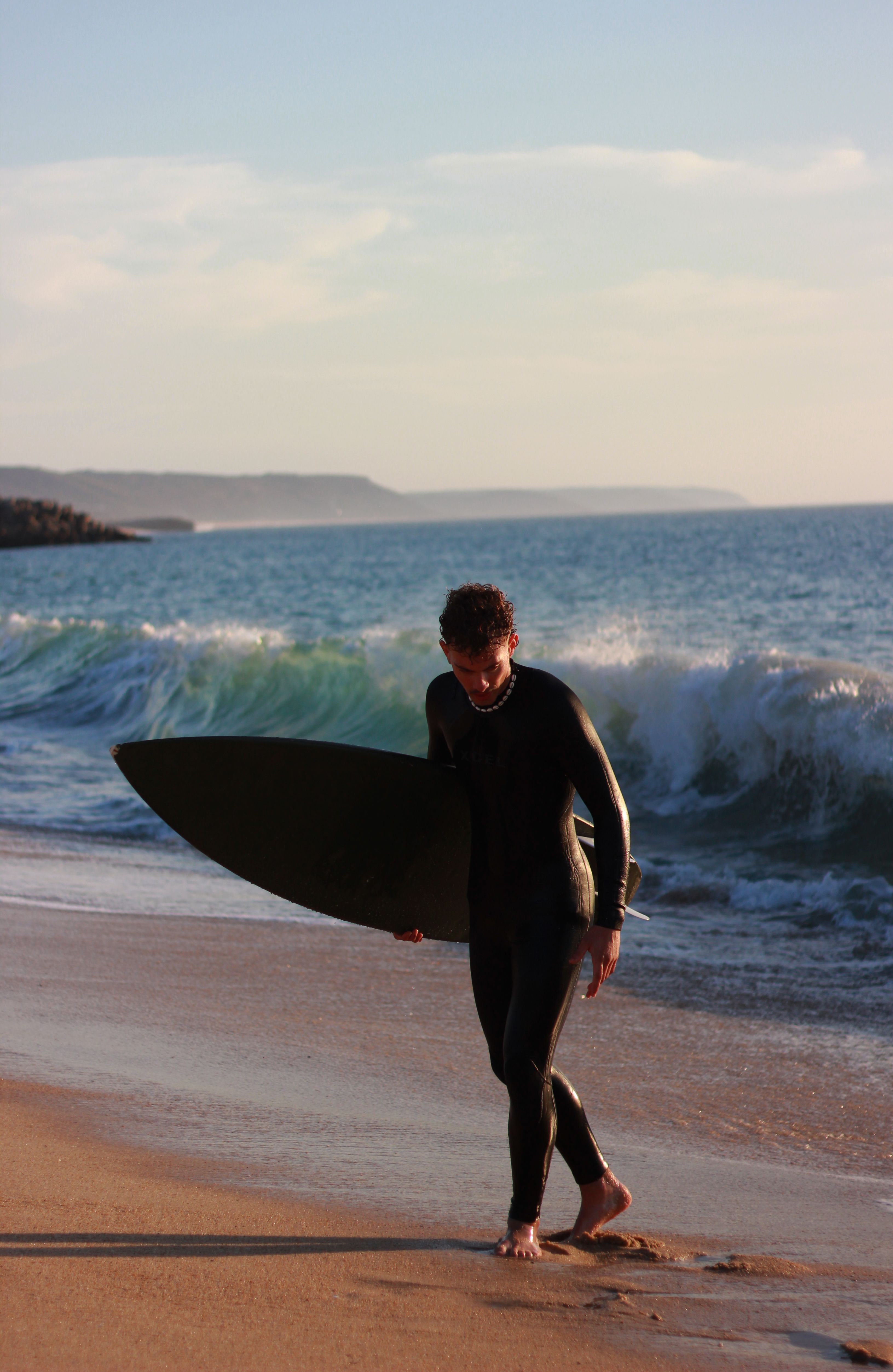 Surfer Walking on Nazaré Beach at Sunset · Free Stock Photo