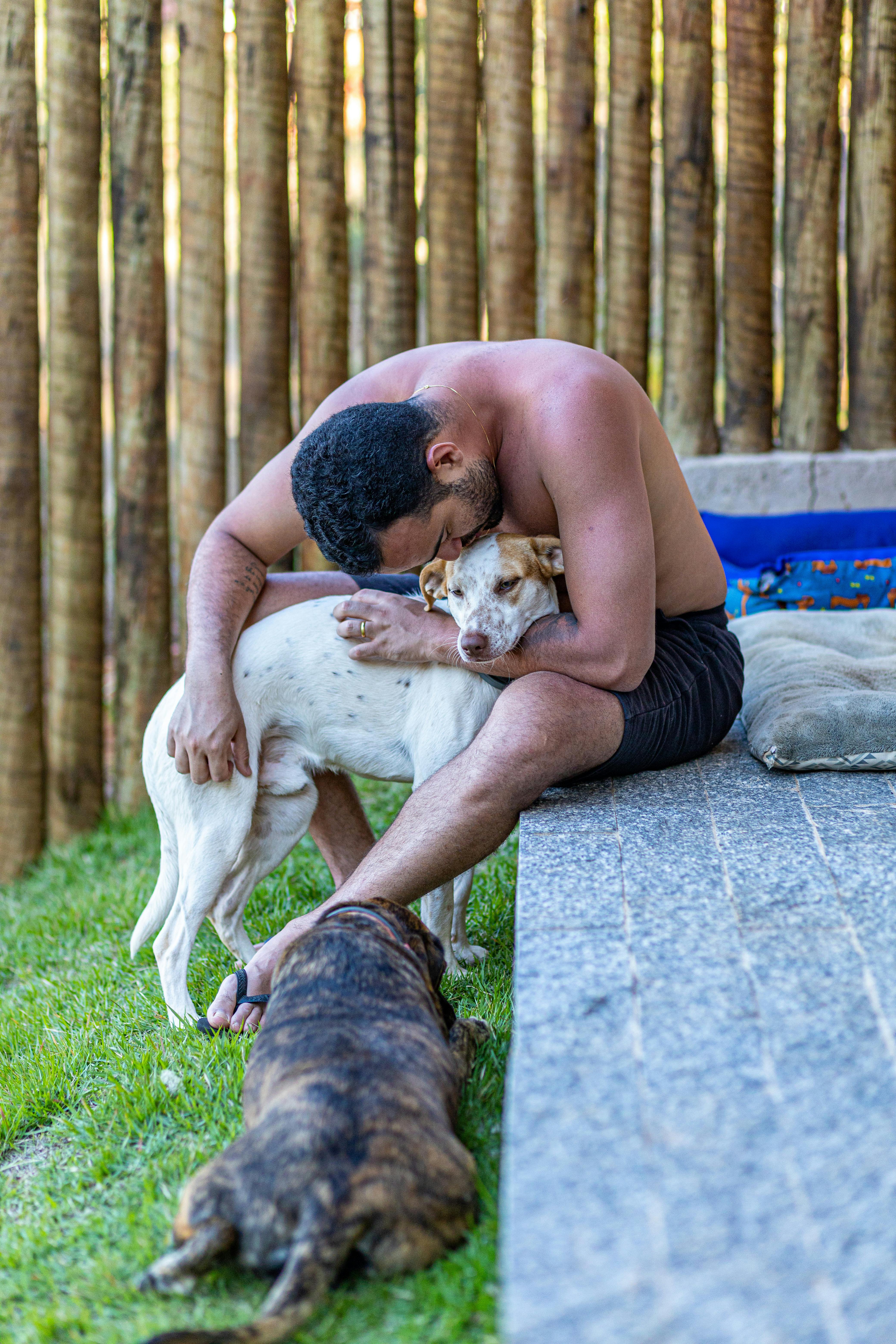 Man Hugging Dogs Outdoors in Relaxing Setting · Free Stock Photo