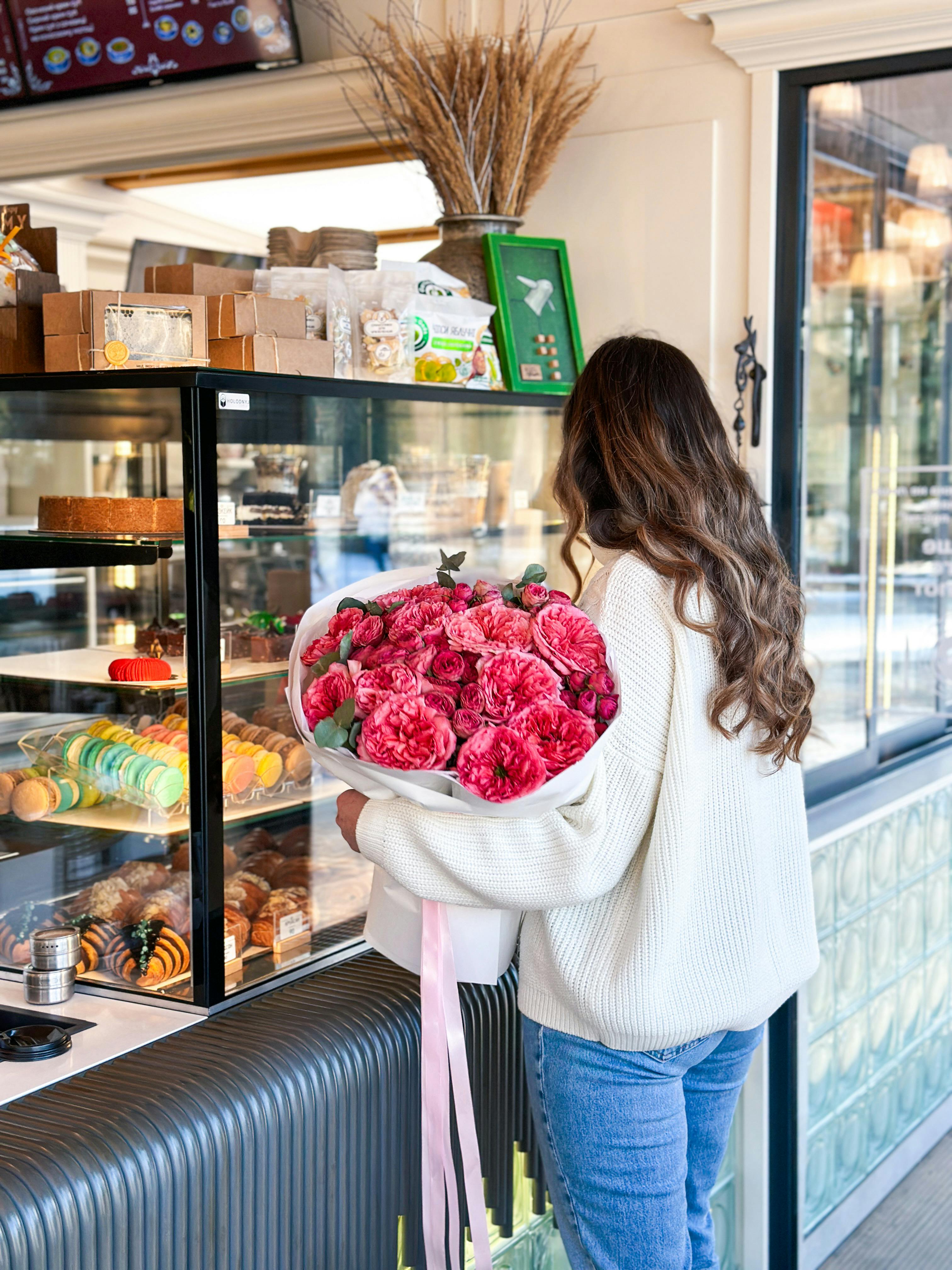 Woman Holding Pink Flowers in Bakery Interior · Free Stock Photo