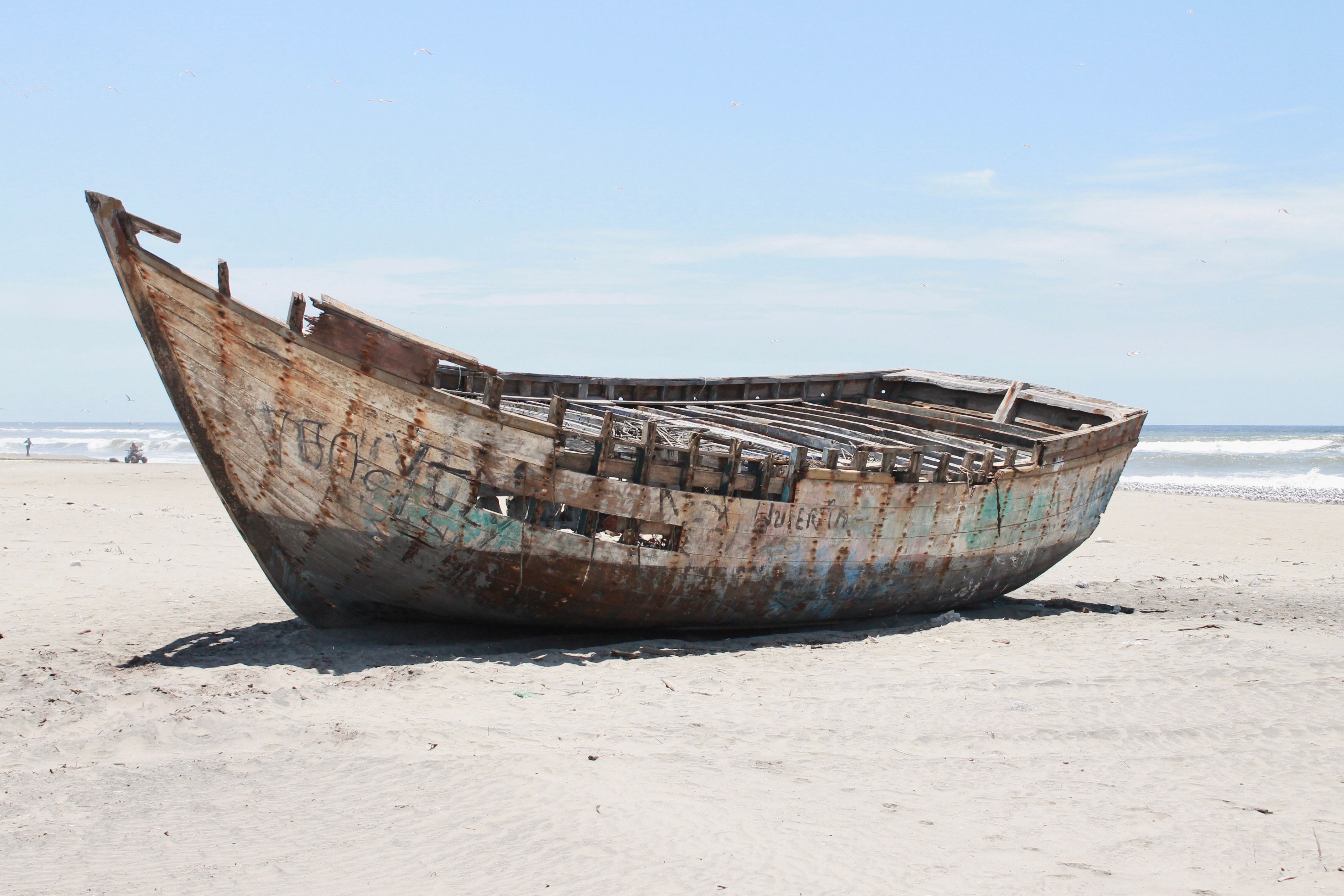 Rustic boat wreck on sandy beach under clear sky · Free Stock Photo