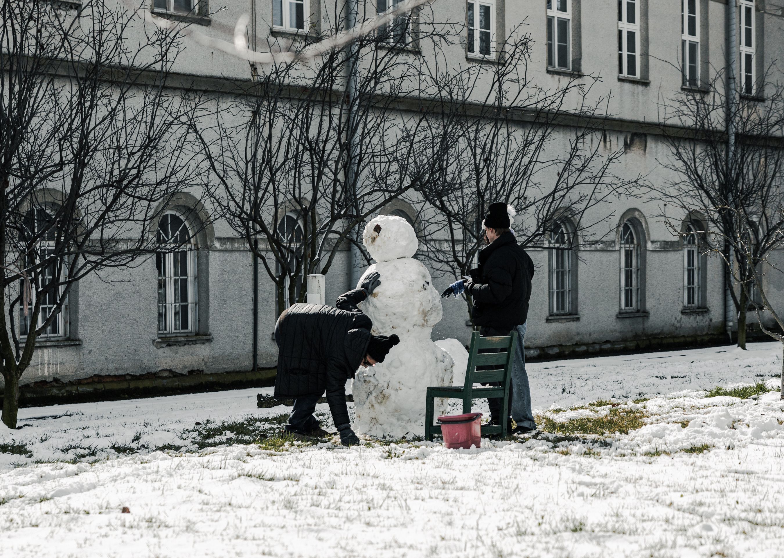 Two People Building a Snowman in Urban Winter Scene · Free Stock Photo