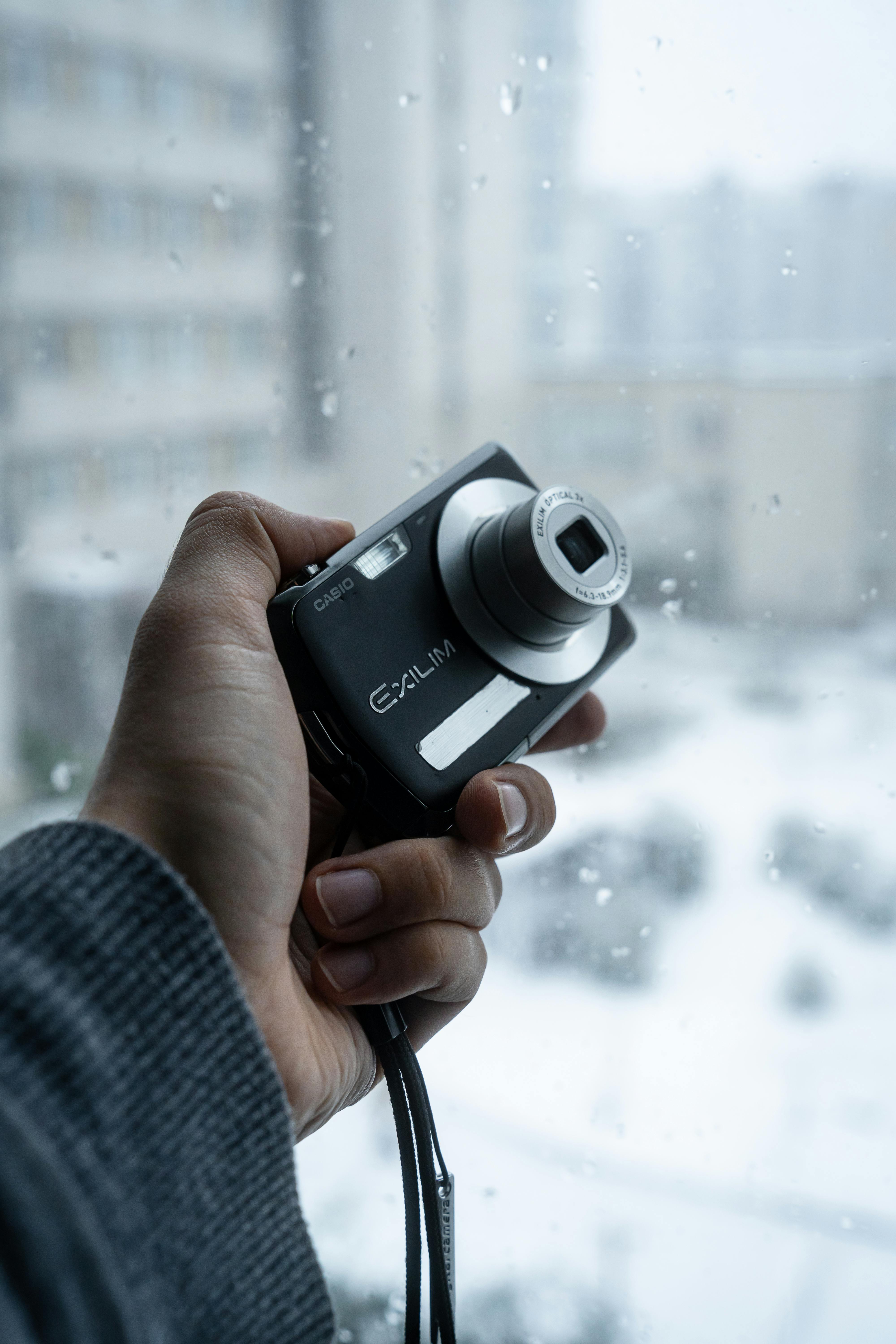 Hand Holding Digital Camera by Snowy Window · Free Stock Photo