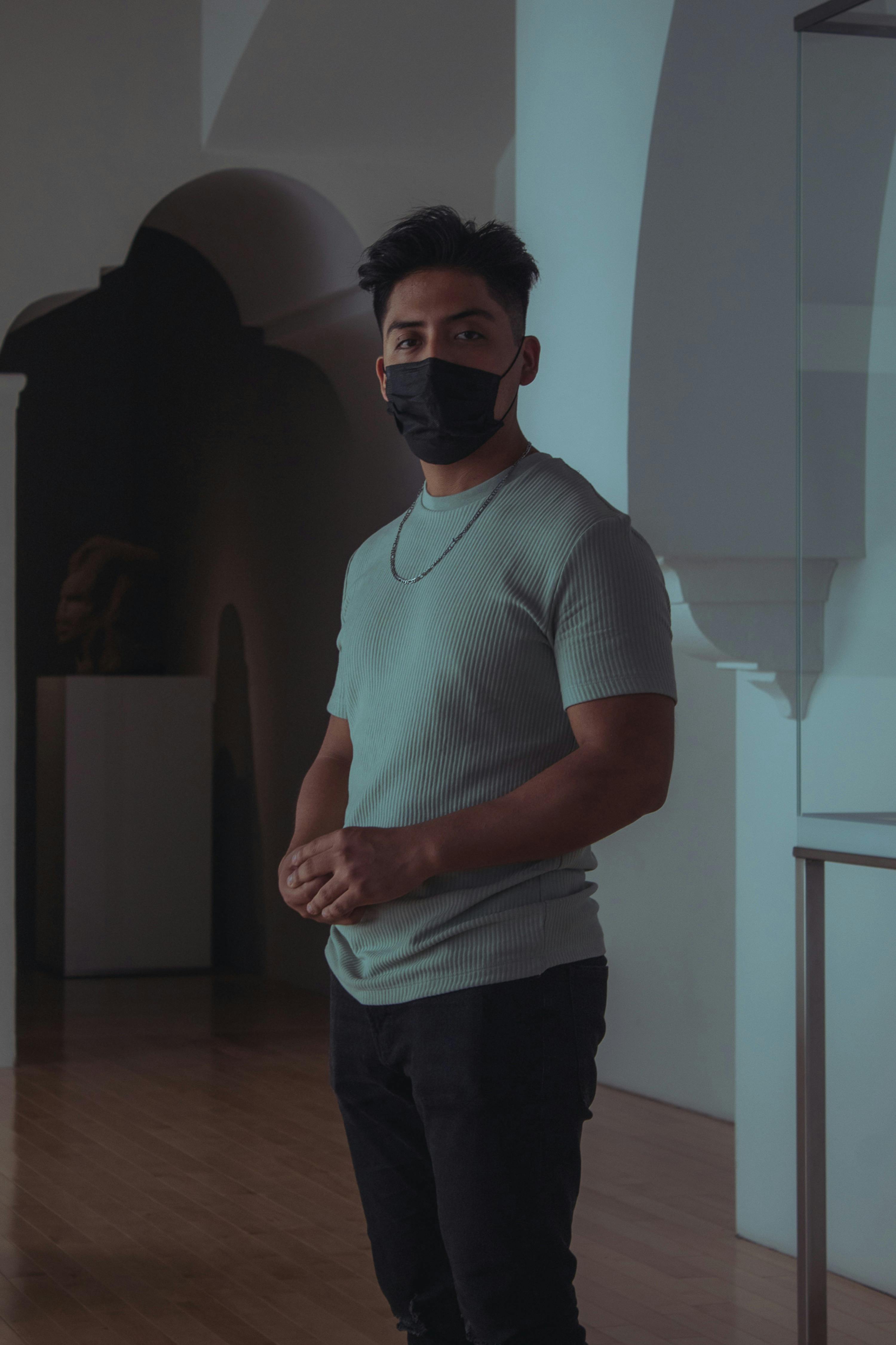 Man in Mask Standing Indoors in Dim Lighting · Free Stock Photo