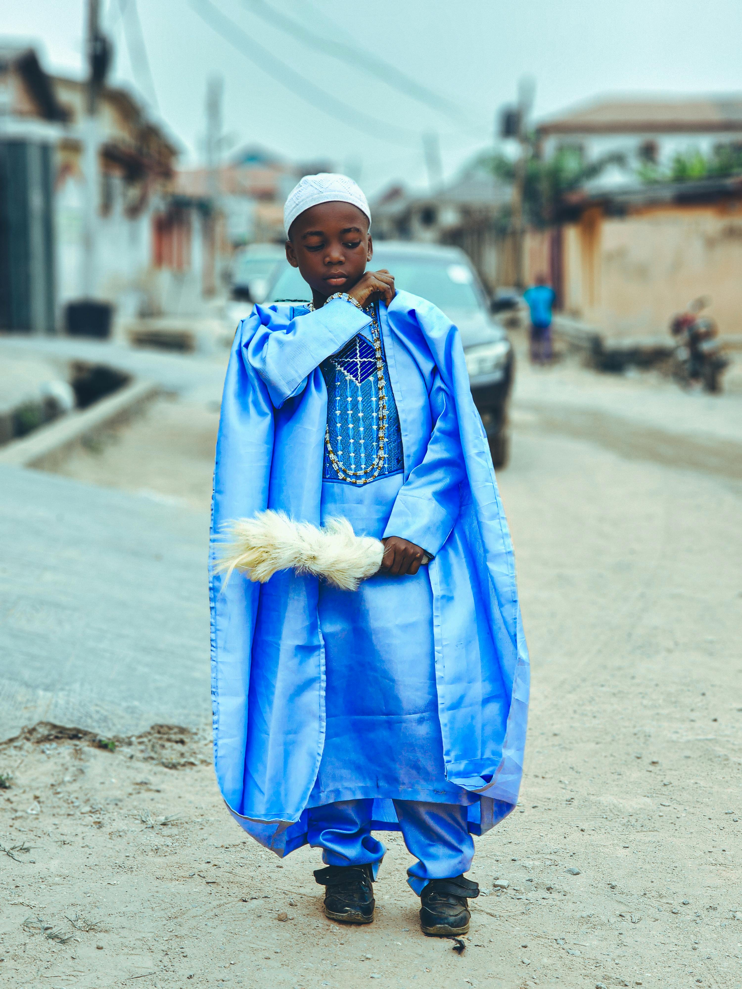 Young boy in traditional blue attire on city street · Free Stock Photo