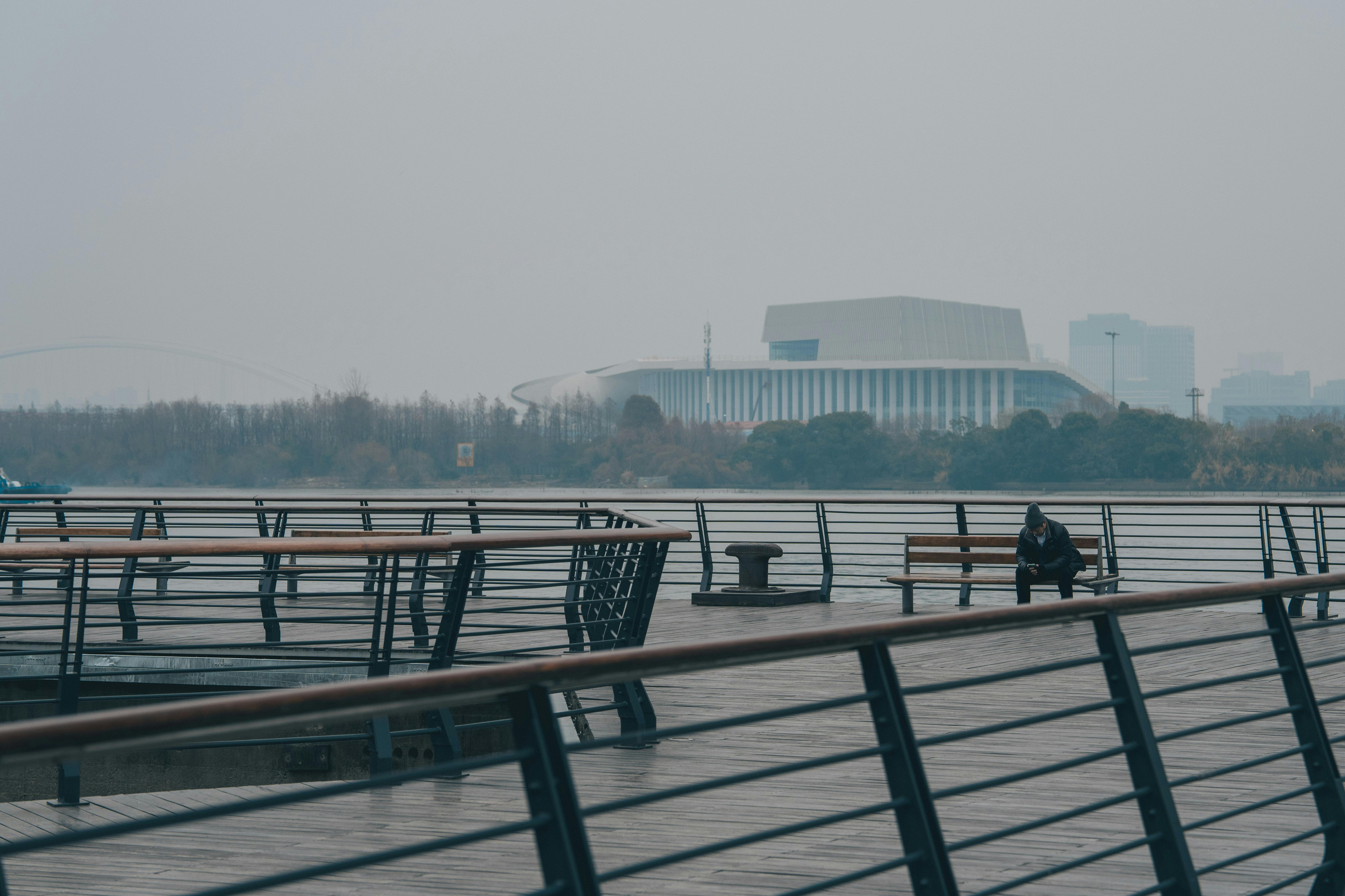 Solitary figure on misty riverside boardwalk · Free Stock Photo