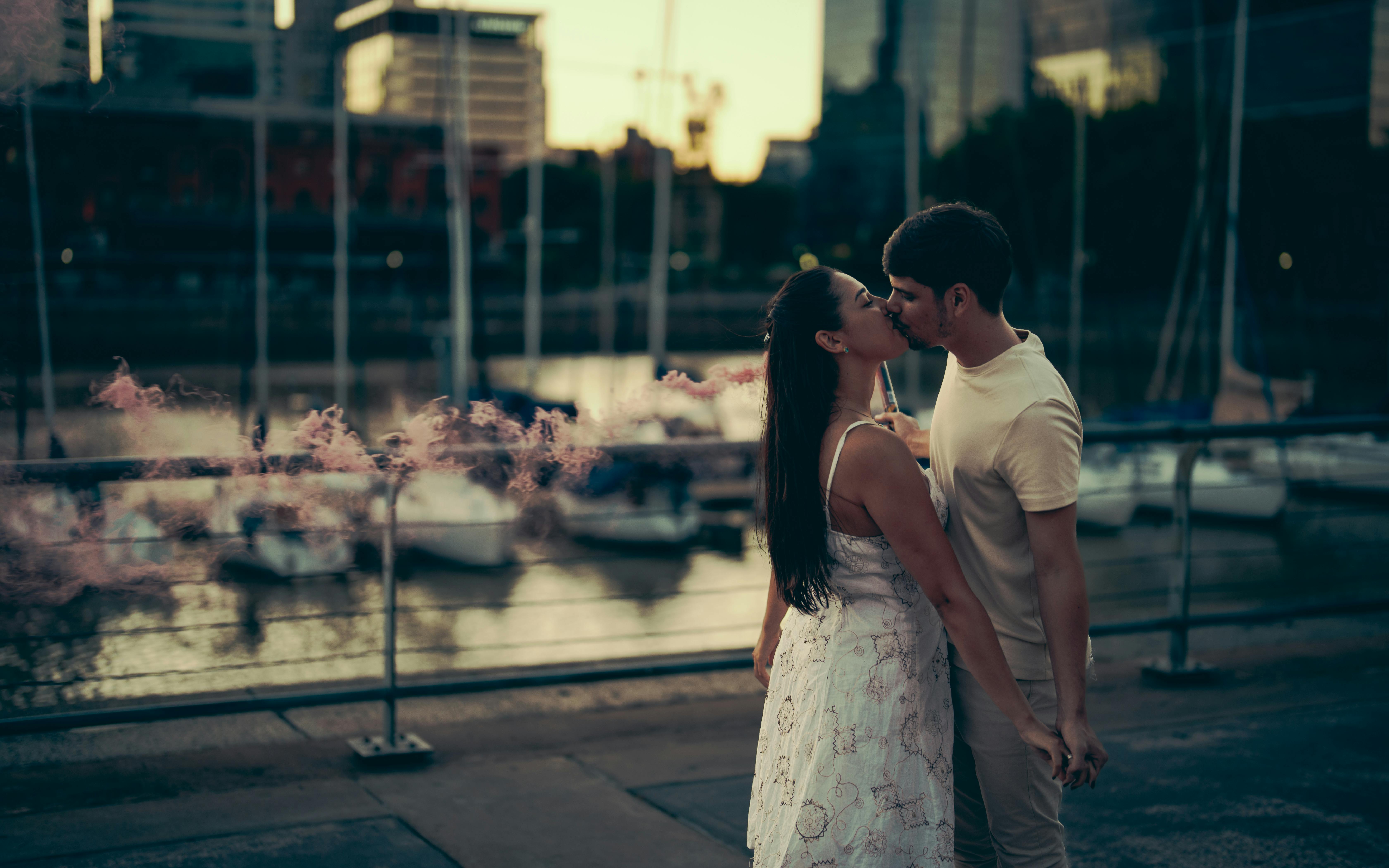 Romantic Couple Kissing by the Waterfront at Sunset · Free Stock Photo