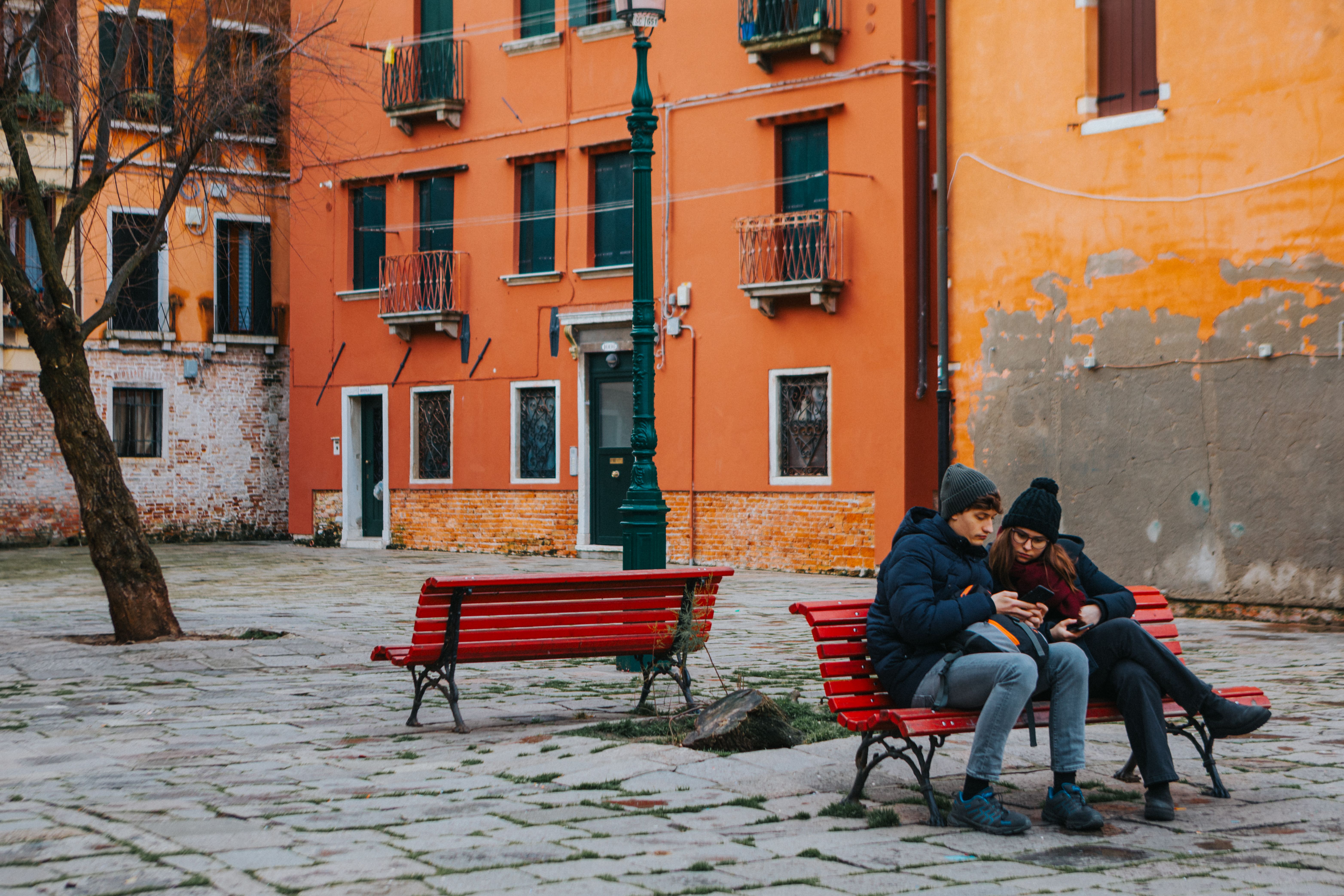 Young Couple Relaxing on Red Benches in Urban Square · Free Stock Photo