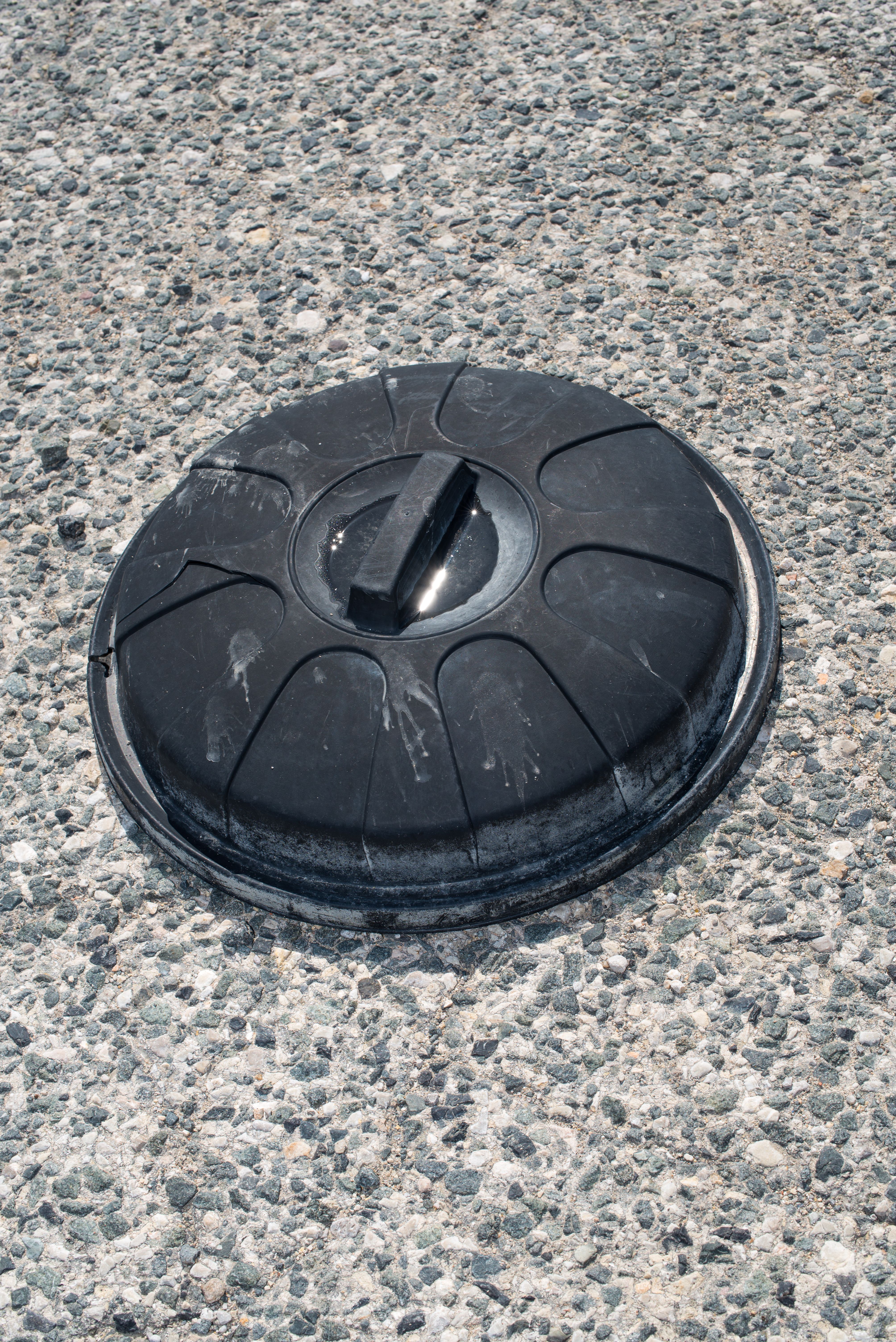Black Trash Can Lid on Textured Pavement · Free Stock Photo
