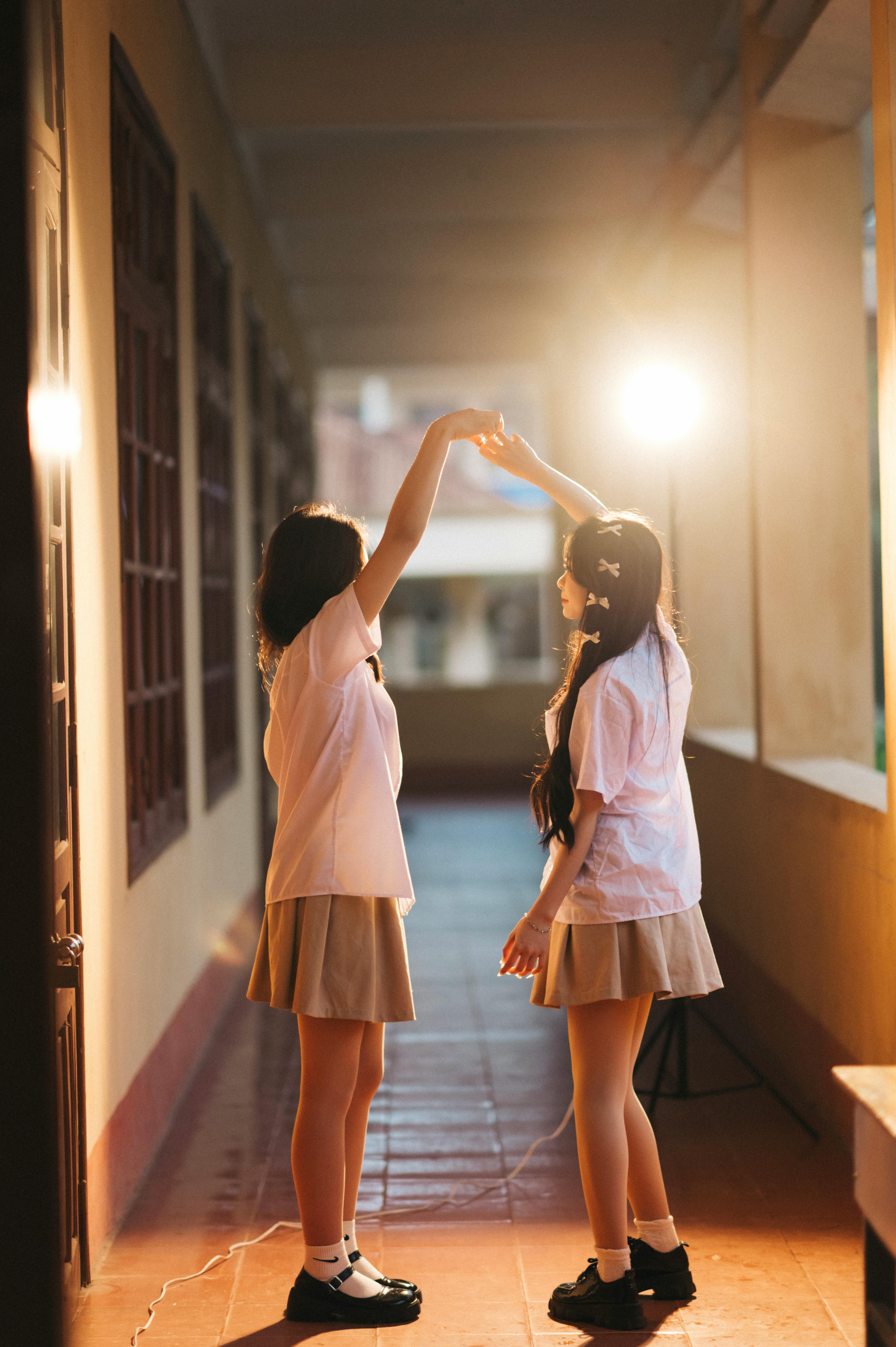 Two schoolgirls dancing in sunlight corridor scene · Free Stock Photo