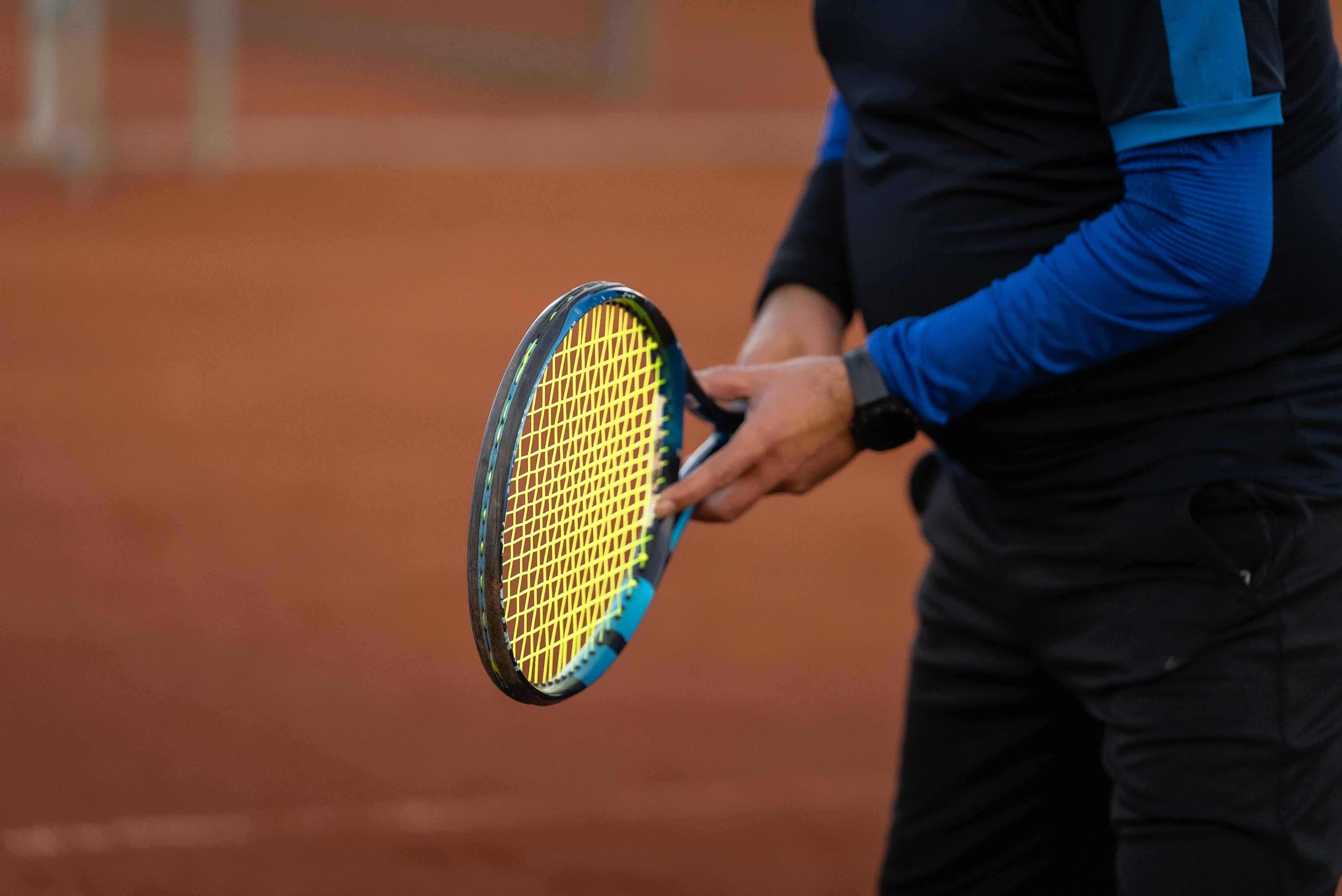 Tennis player gripping racket on clay court · Free Stock Photo