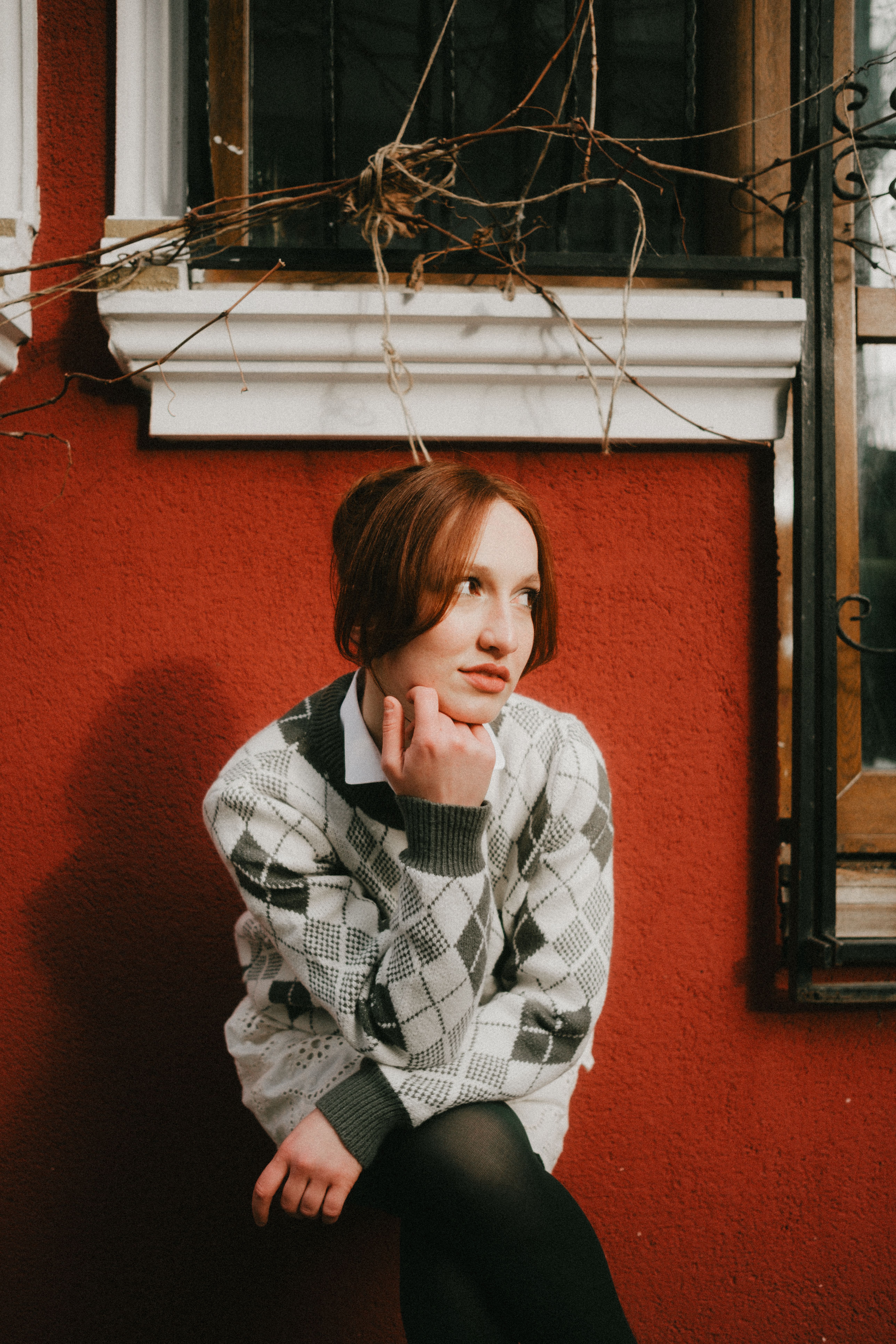 Reflective Woman in Argyle Sweater by Red Wall · Free Stock Photo