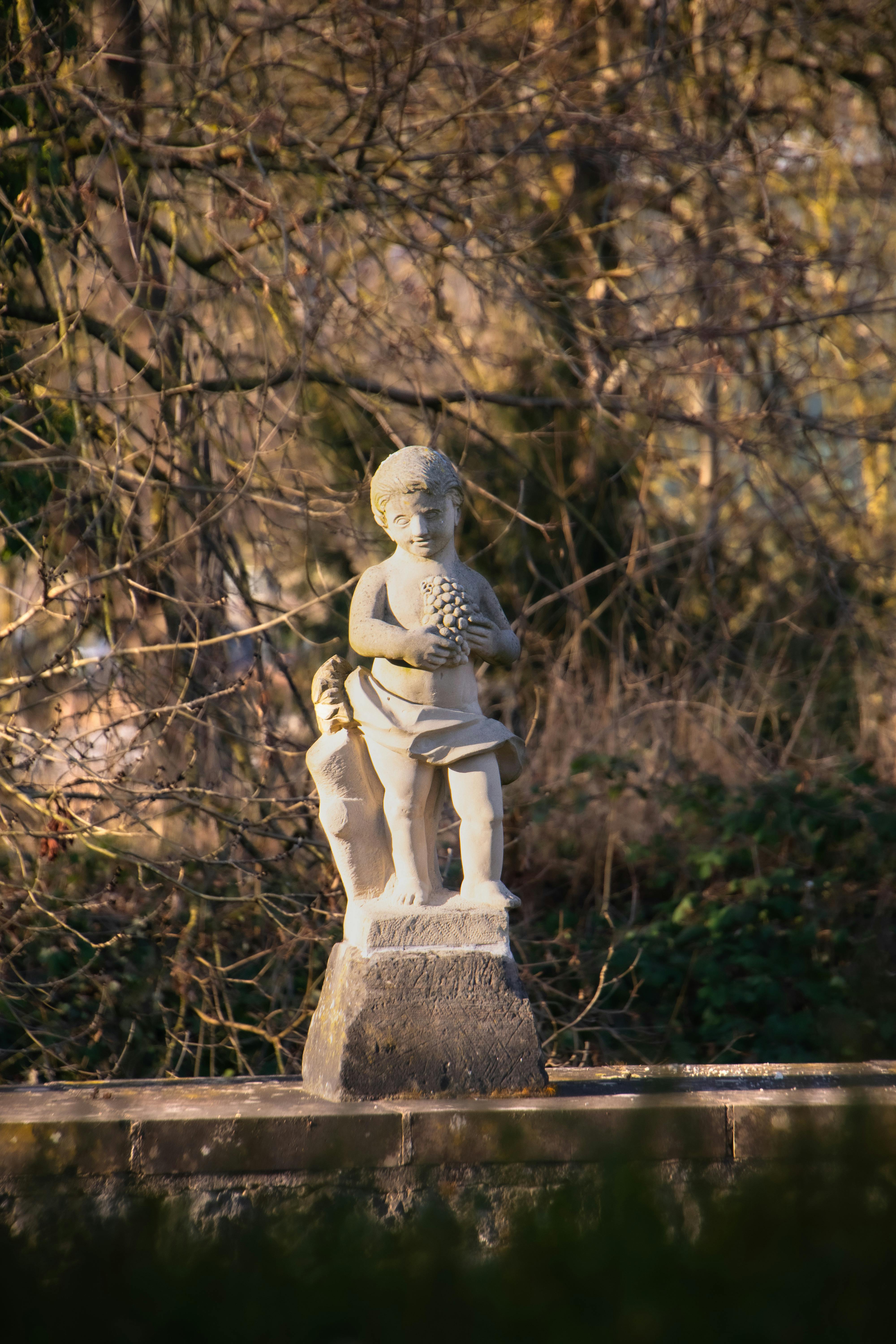 Stone statue of child in serene outdoor setting · Free Stock Photo