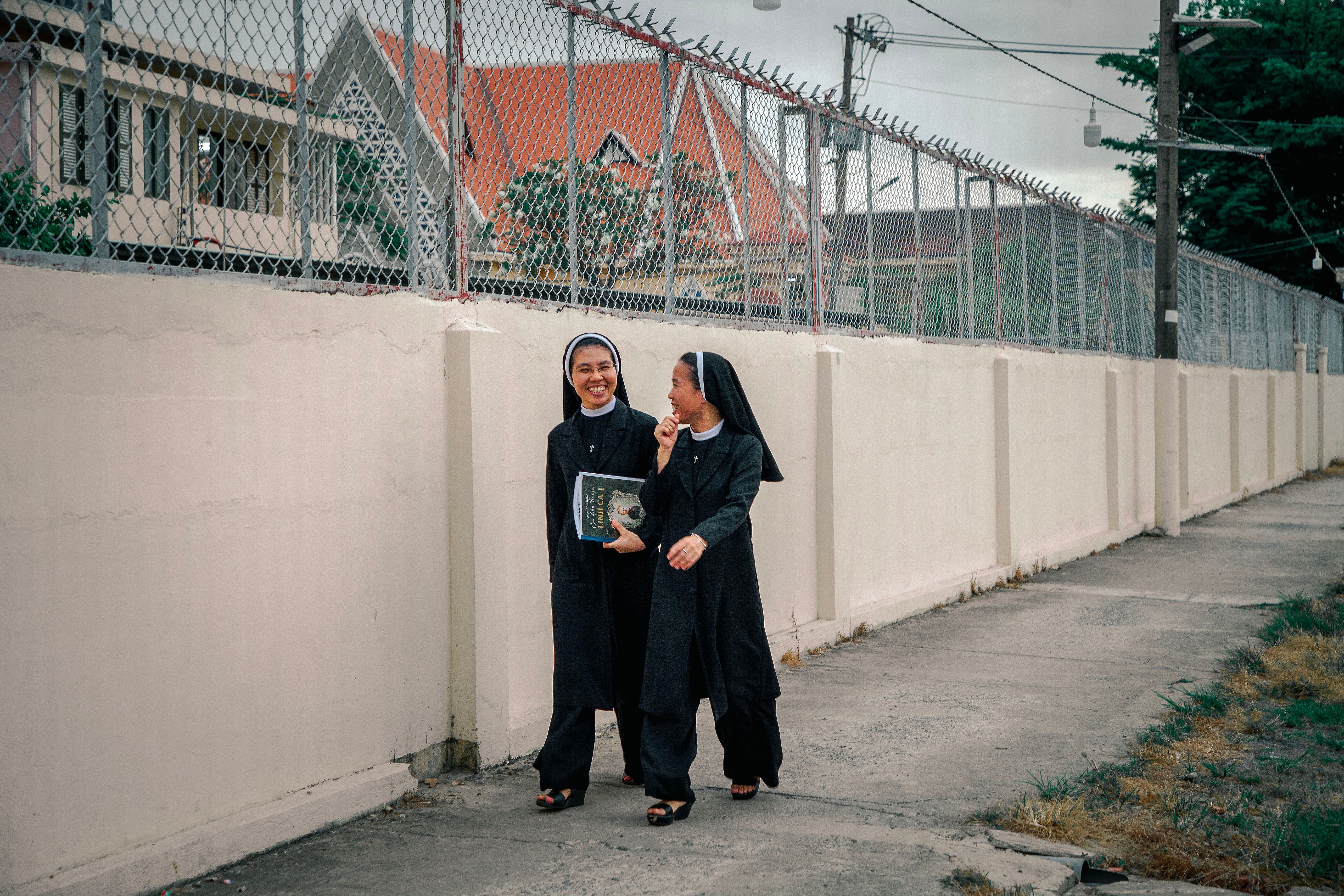 Smiling Nuns Walking Alongside Fence Outdoors · Free Stock Photo