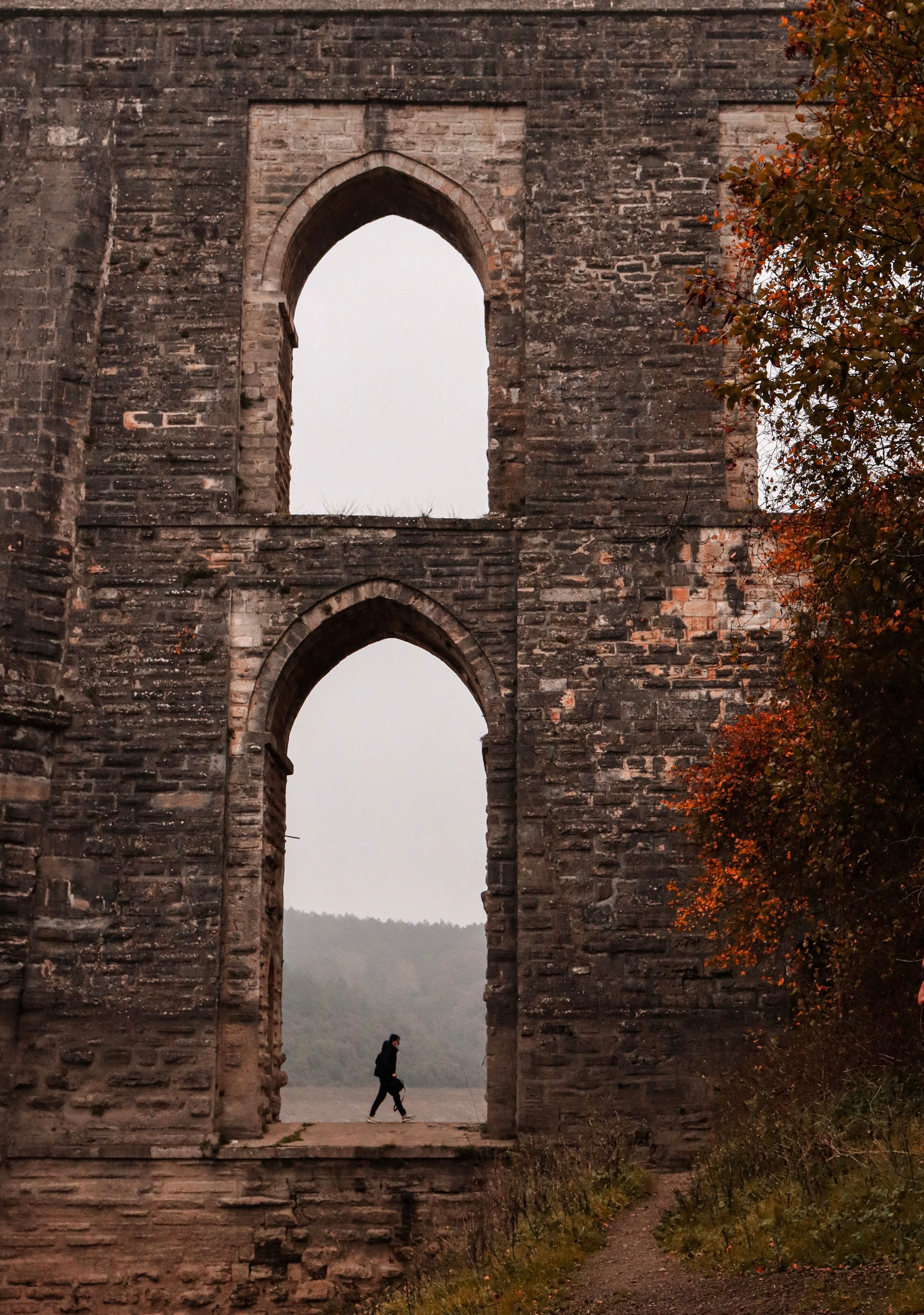 Silhouetted Figure Walking Under Stone Arches · Free Stock Photo