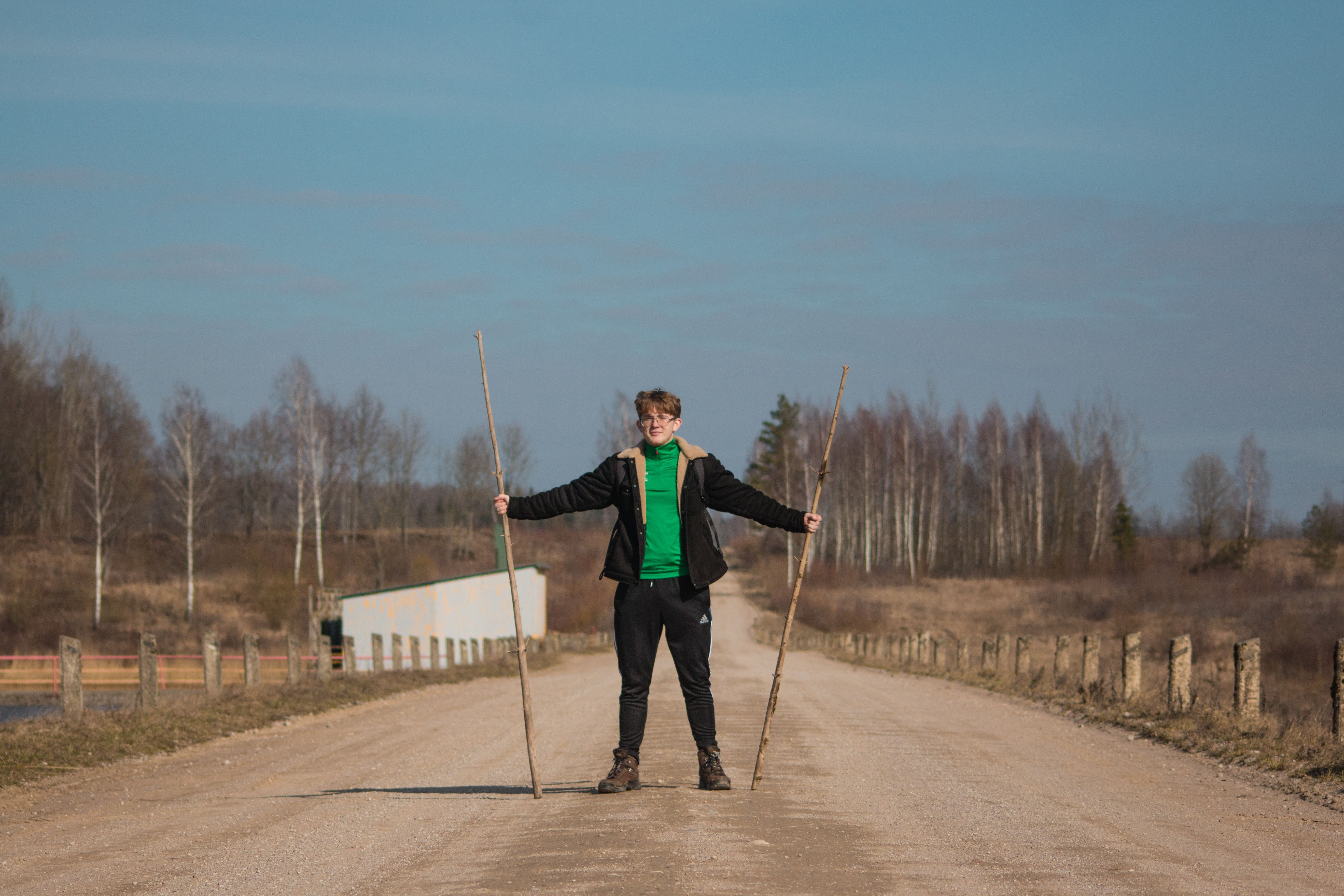 Young man holding sticks on rural dirt road · Free Stock Photo