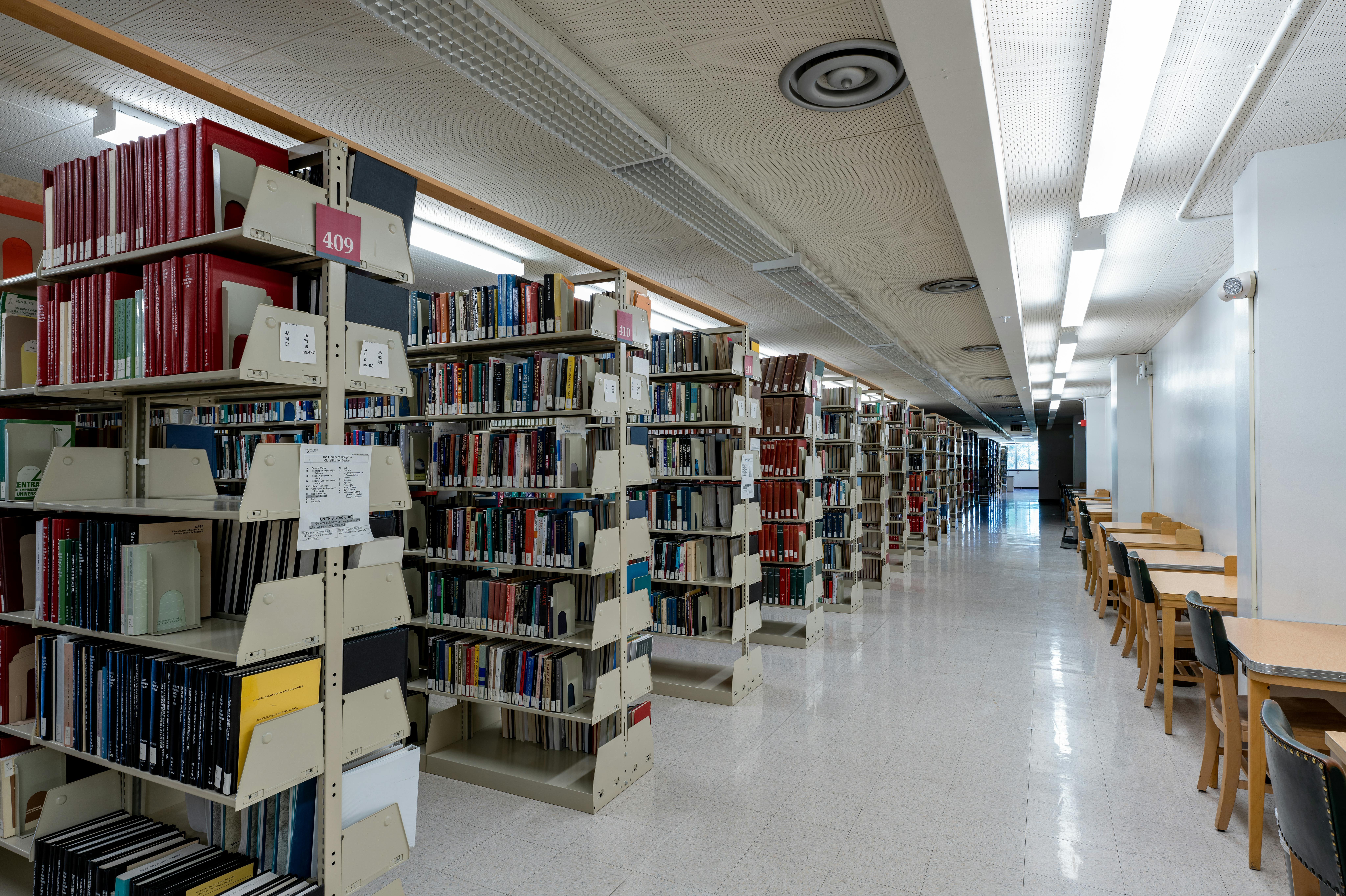 Spacious Library Aisle with Bookshelves and Study Tables · Free Stock Photo