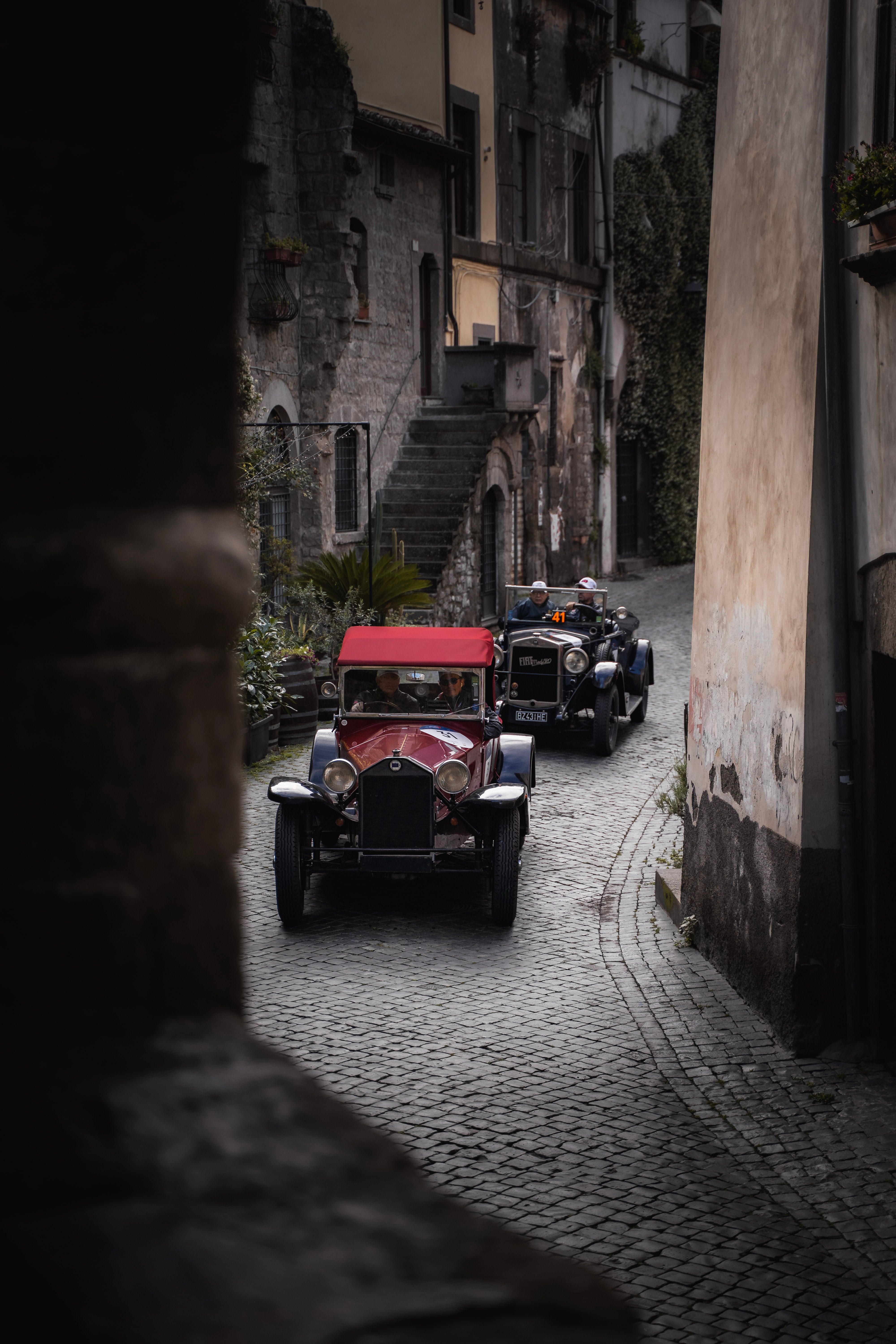 Vintage Cars Driving Through Historic Cobblestone Alley · Free Stock Photo