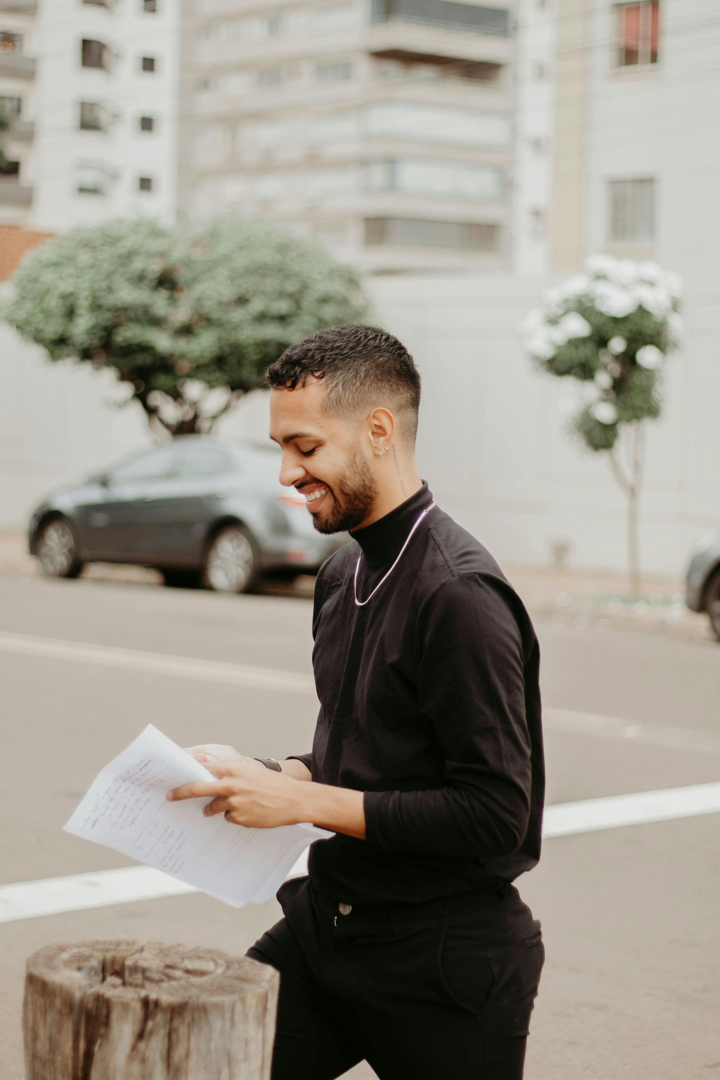 Man Smiling Holding Script in Urban Setting · Free Stock Photo