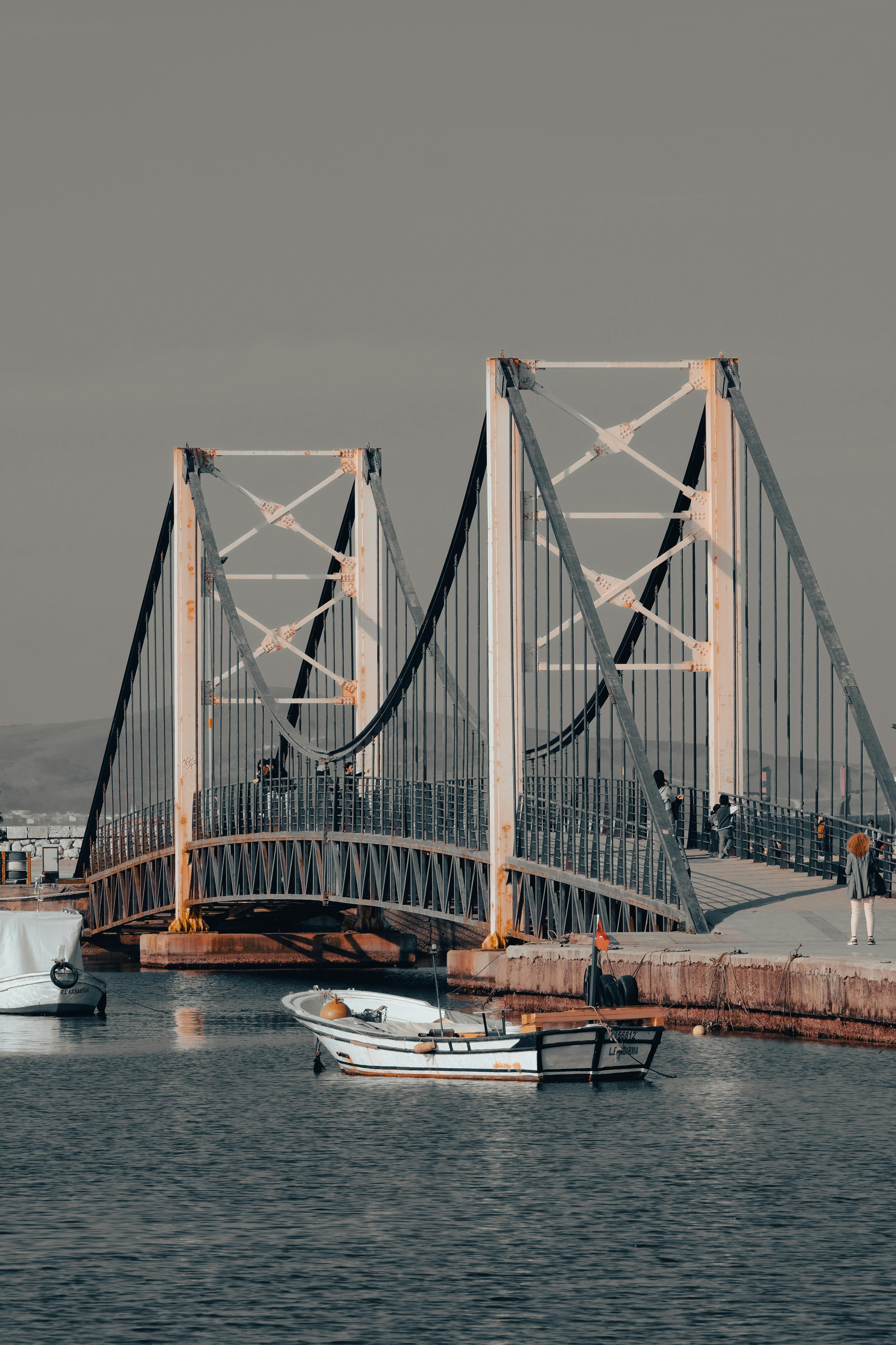 Modern Suspension Bridge with Boats on Calm River · Free Stock Photo