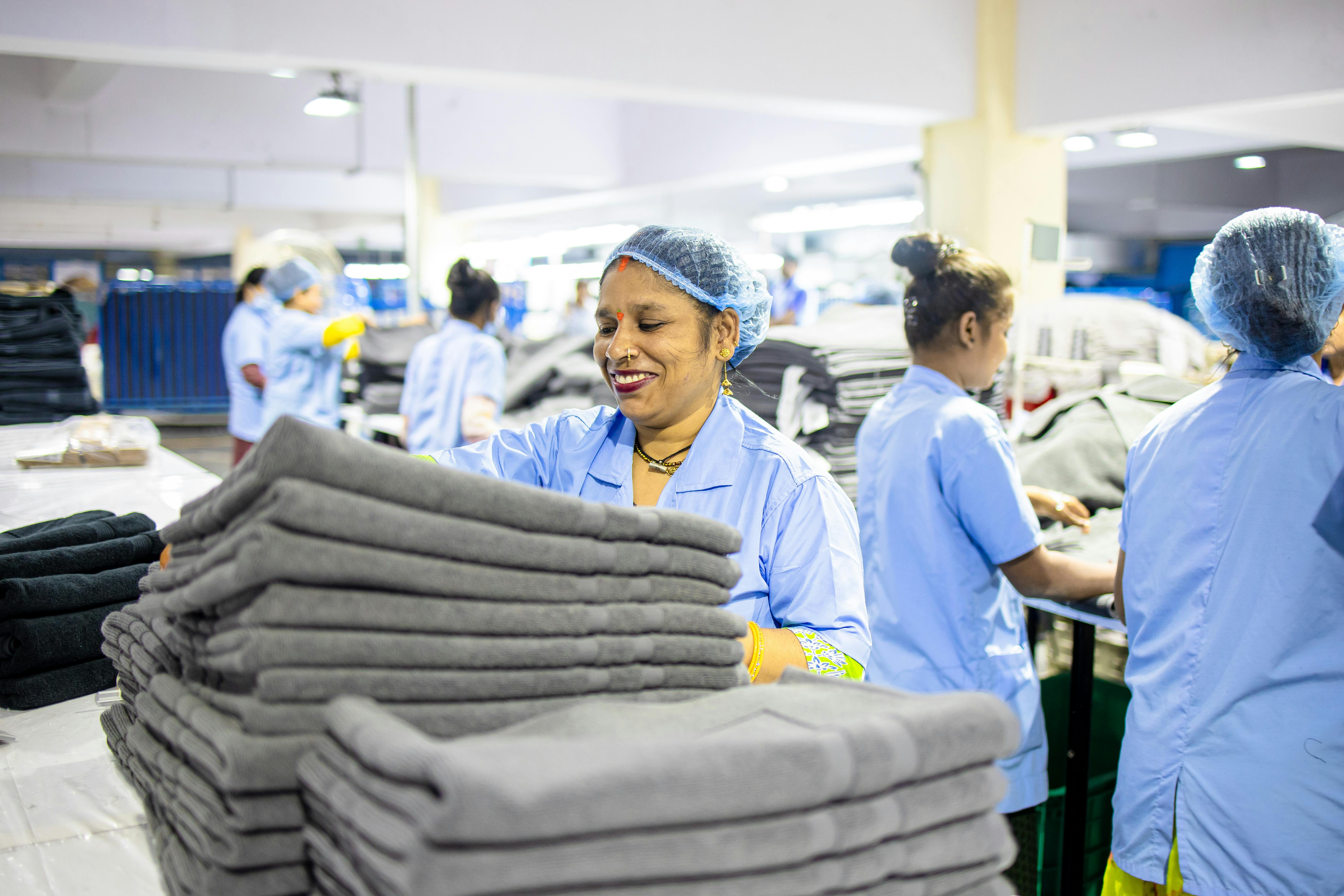 Smiling textile worker stacking folded garments · Free Stock Photo