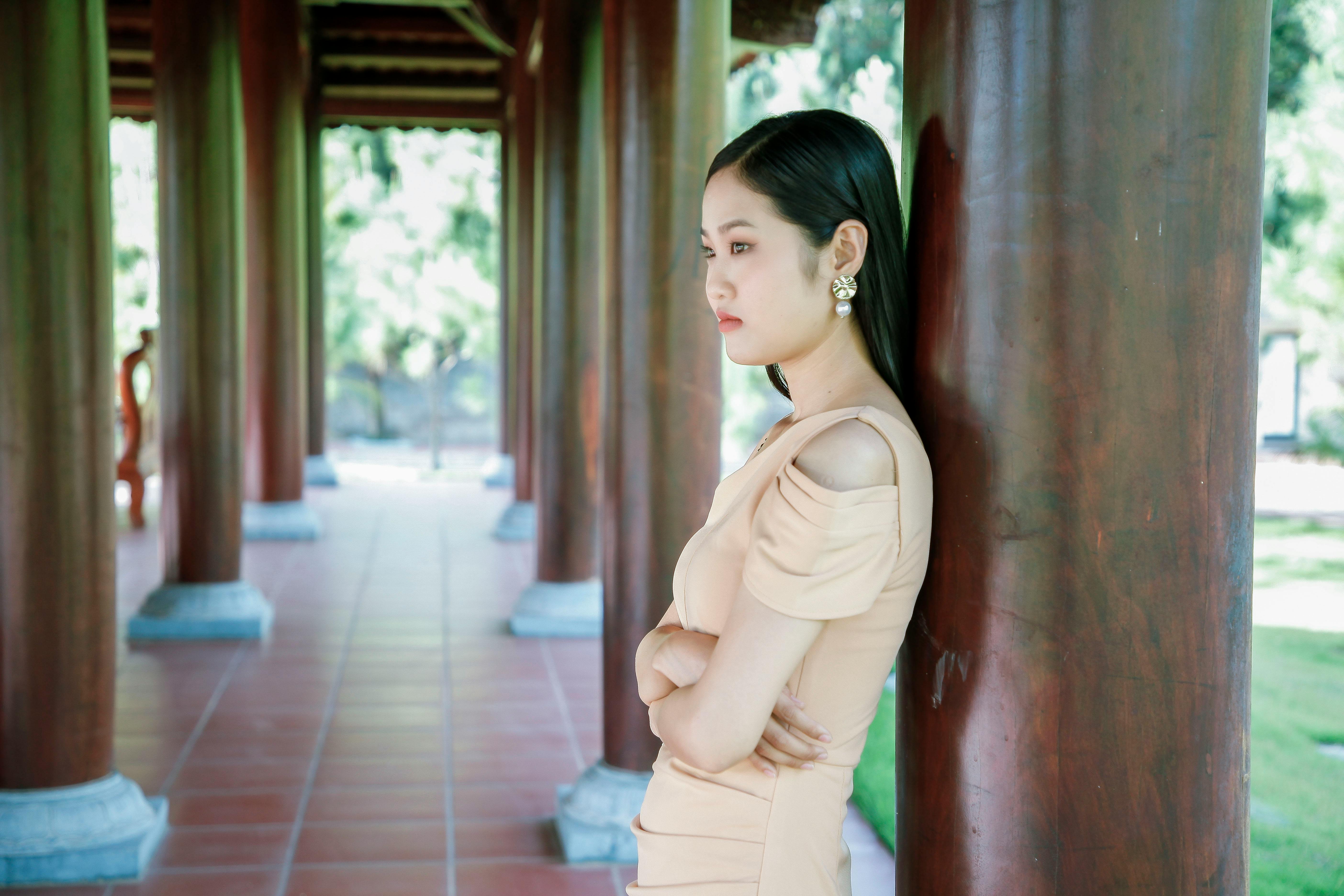Elegant Woman Leaning by Rustic Wooden Pillars · Free Stock Photo