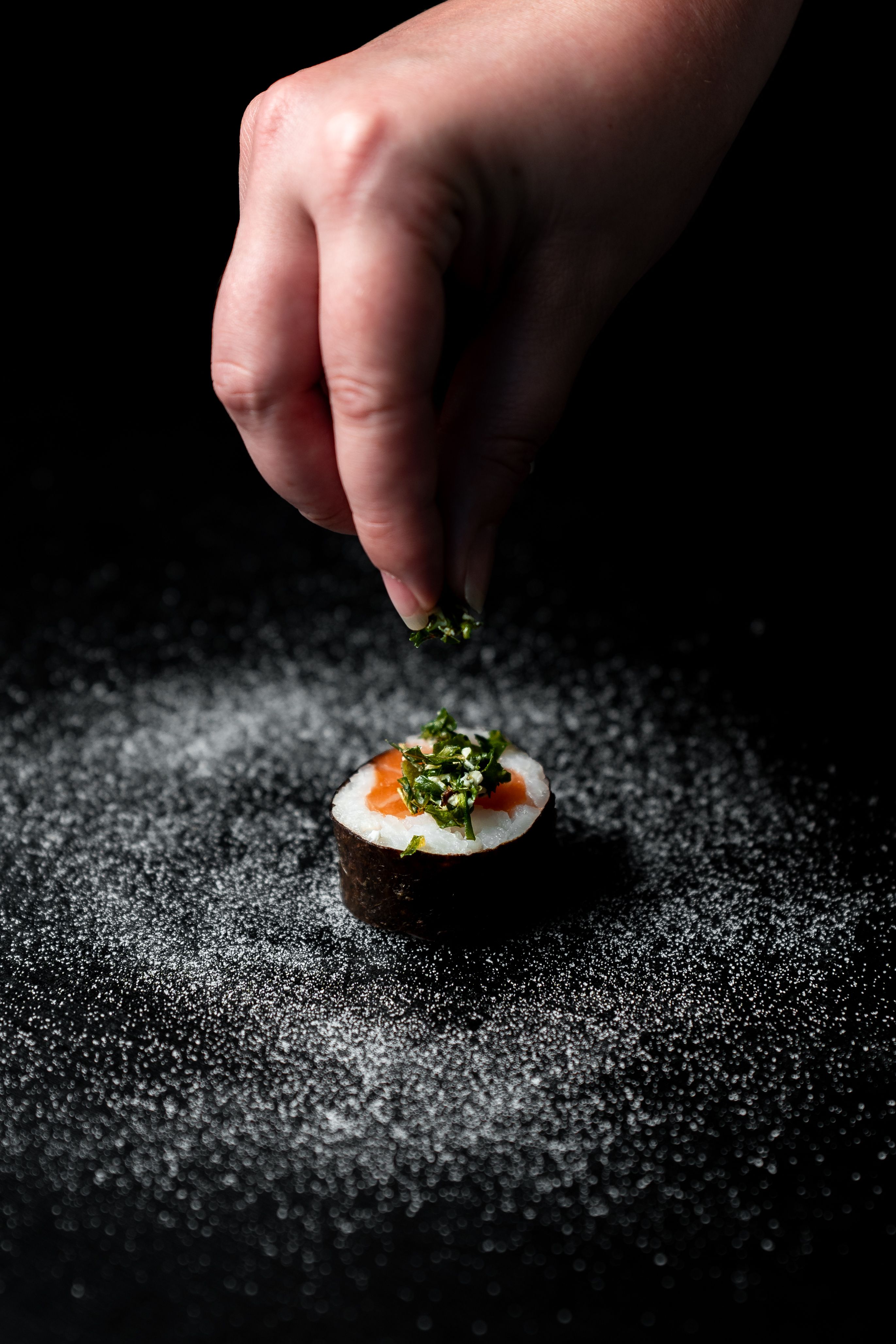 Hand Garnishing Sushi with Herbs on Black Surface · Free Stock Photo