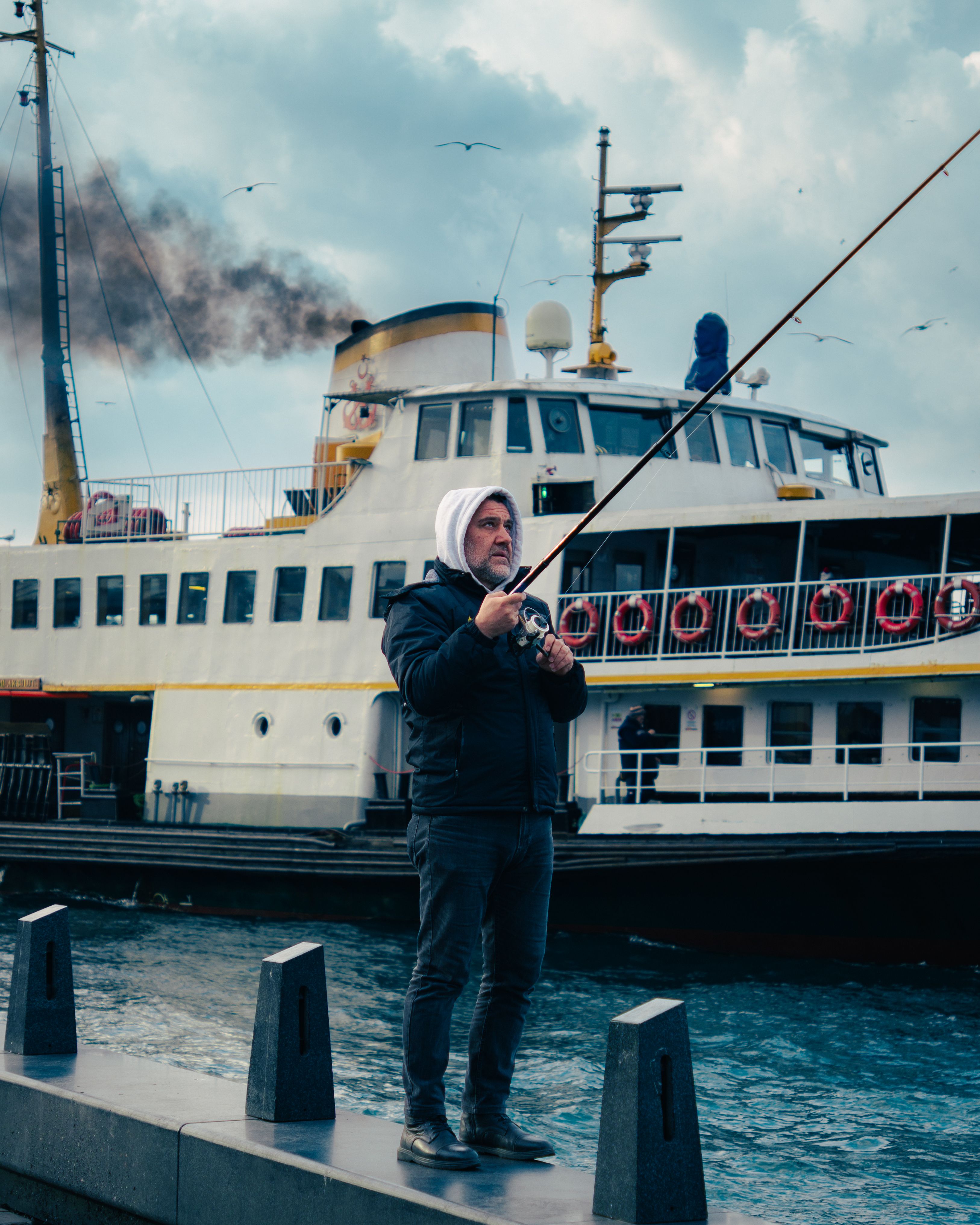 Man Fishing by Ferry in Harbor, Overcast Day · Free Stock Photo