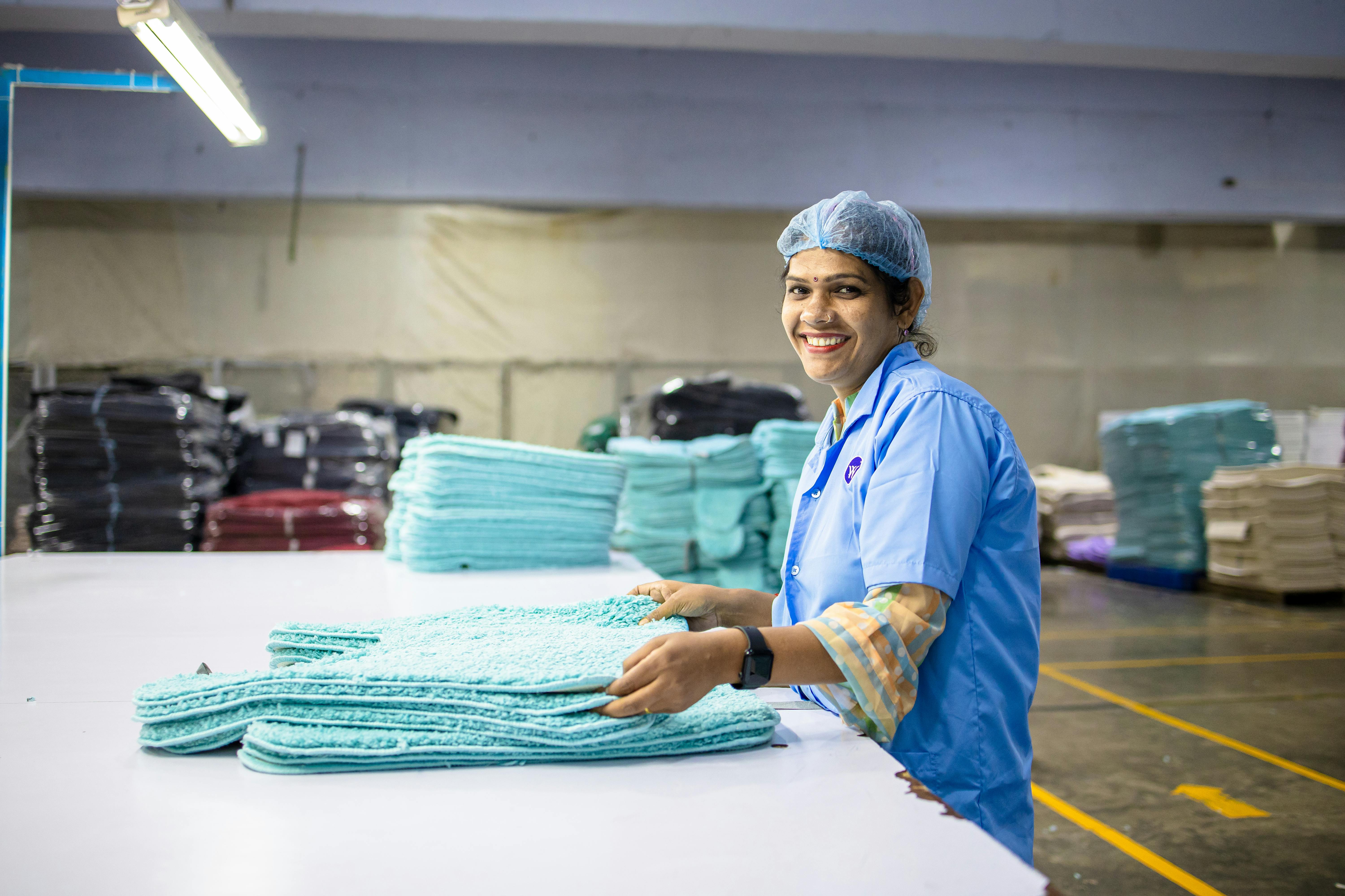 Smiling textile worker folding fabrics in factory · Free Stock Photo
