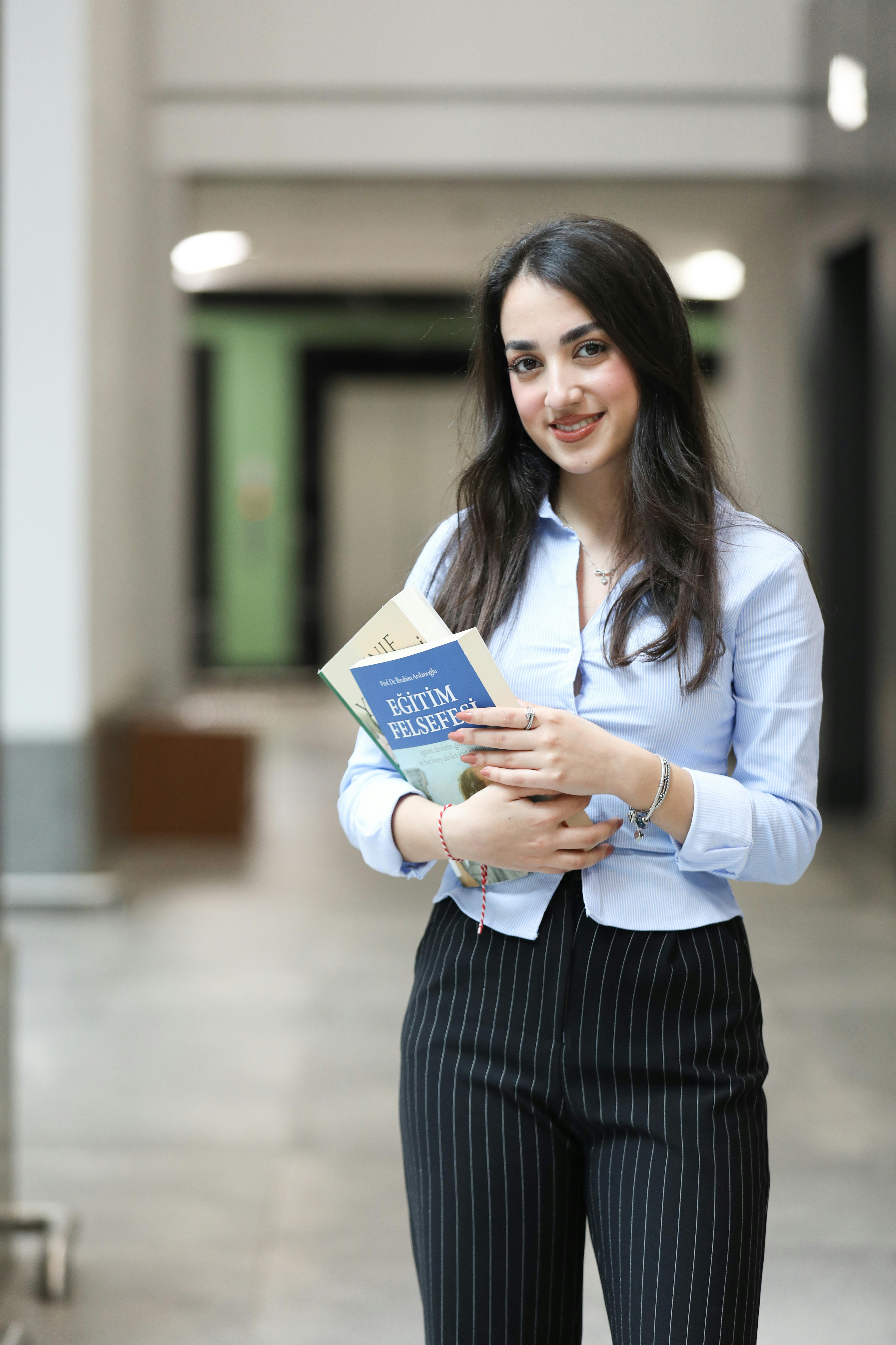 Confident Young Woman Holding Books in Office Corridor · Free Stock Photo