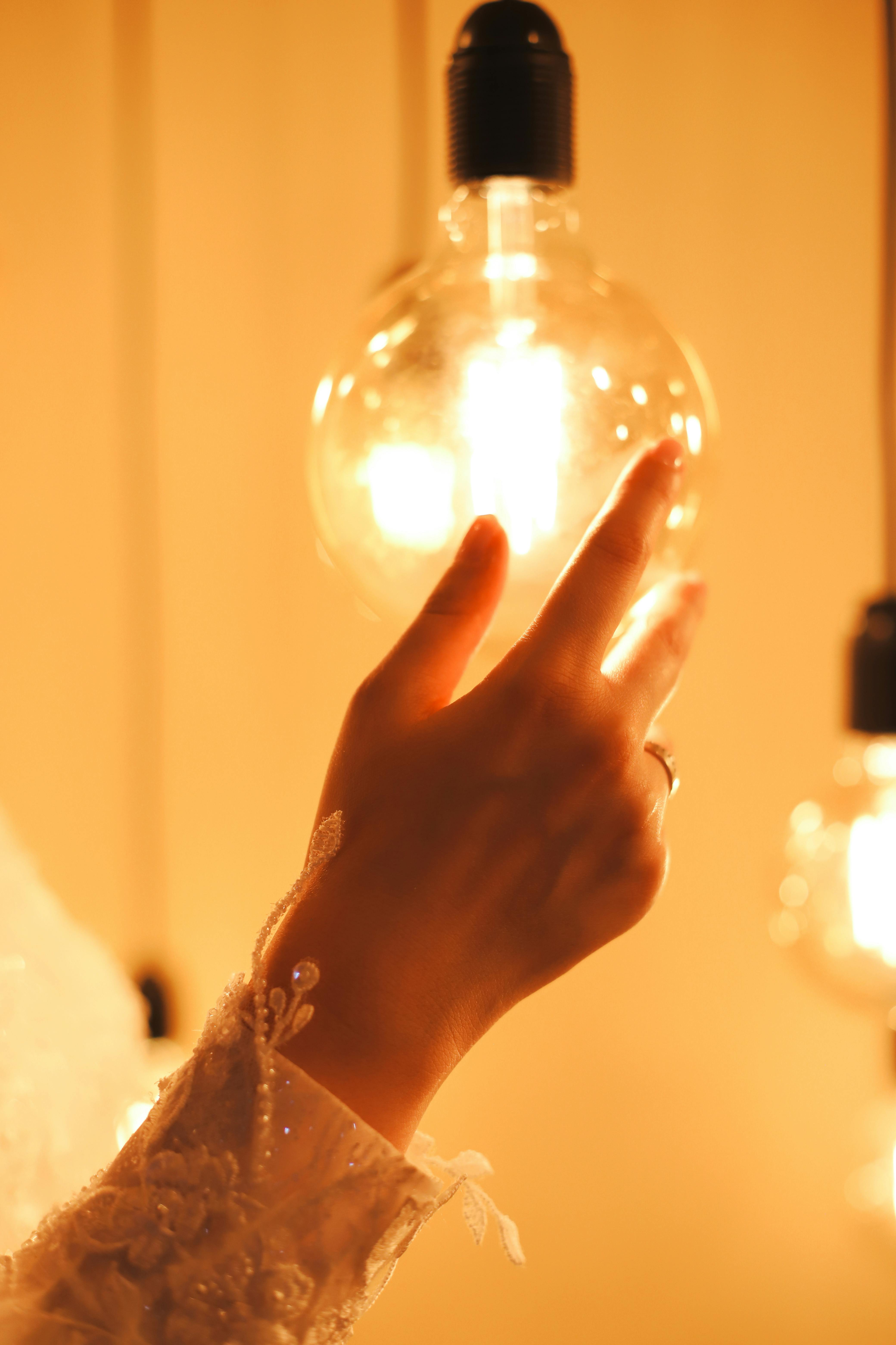Elegant Hand Touching Glowing Light Bulb · Free Stock Photo