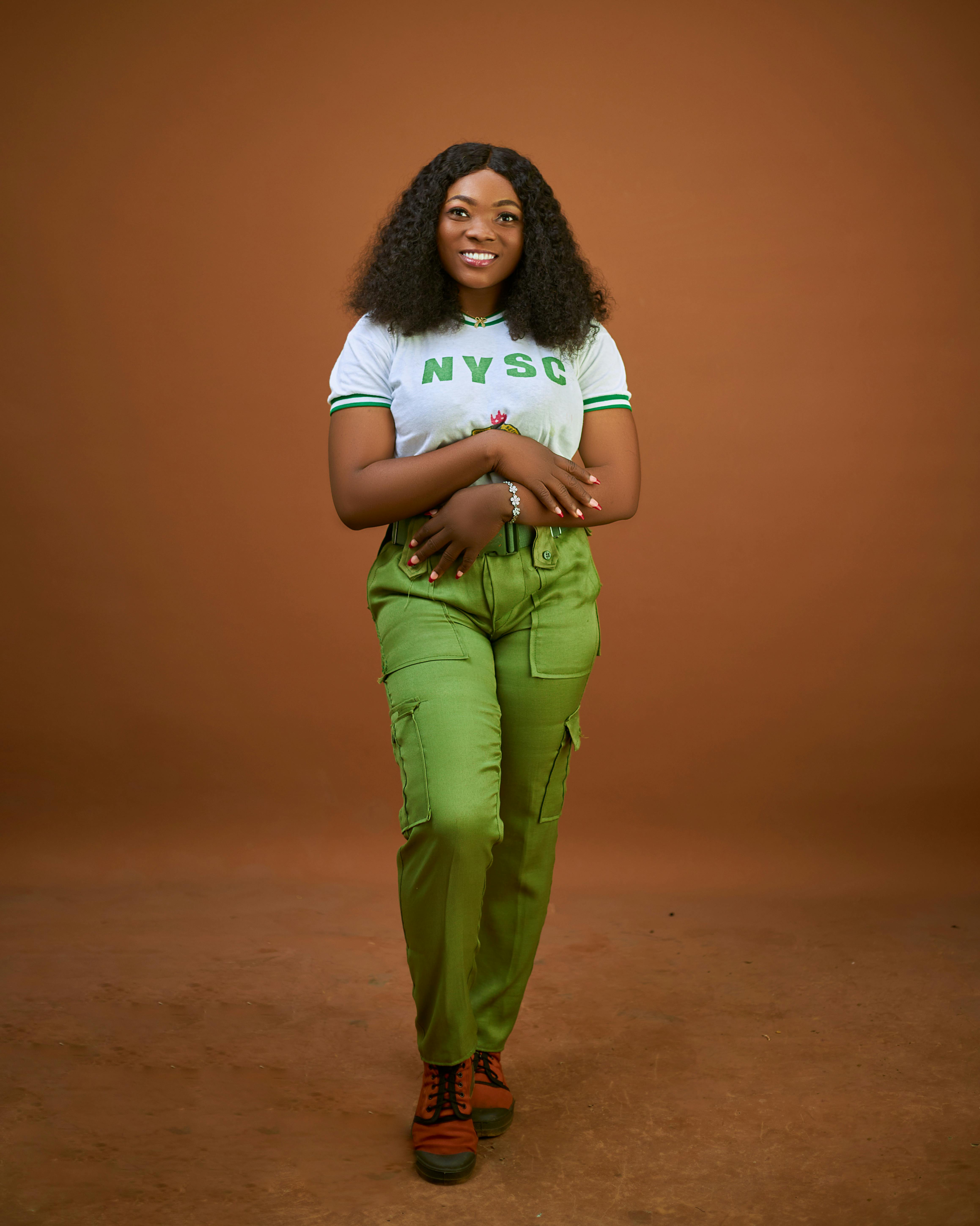 Young Woman in NYSC Attire on Brown Background · Free Stock Photo