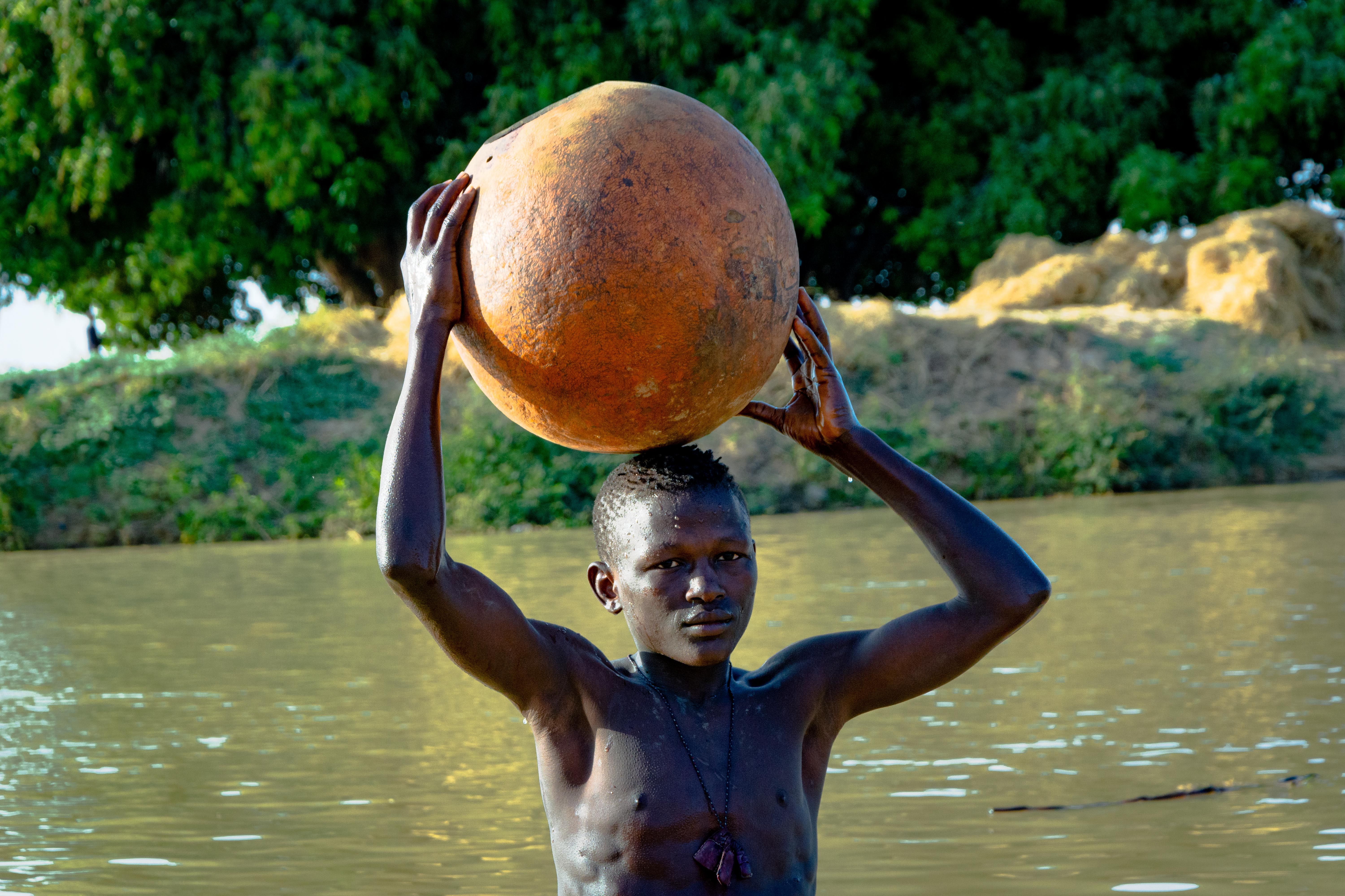 Young Man Carrying Large Pot by River in Nigeria · Free Stock Photo