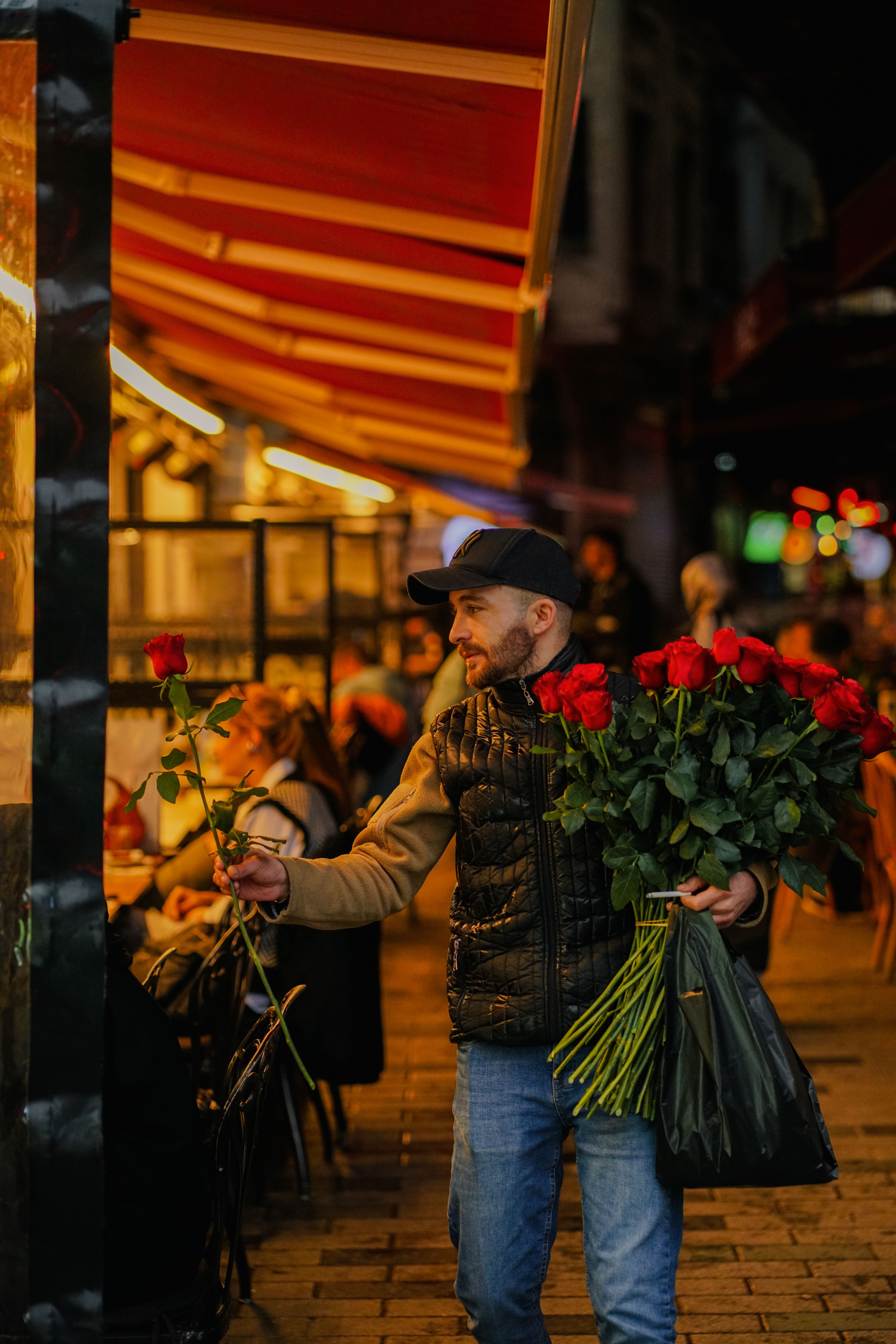 Man Selling Roses at Nighttime Street Café · Free Stock Photo
