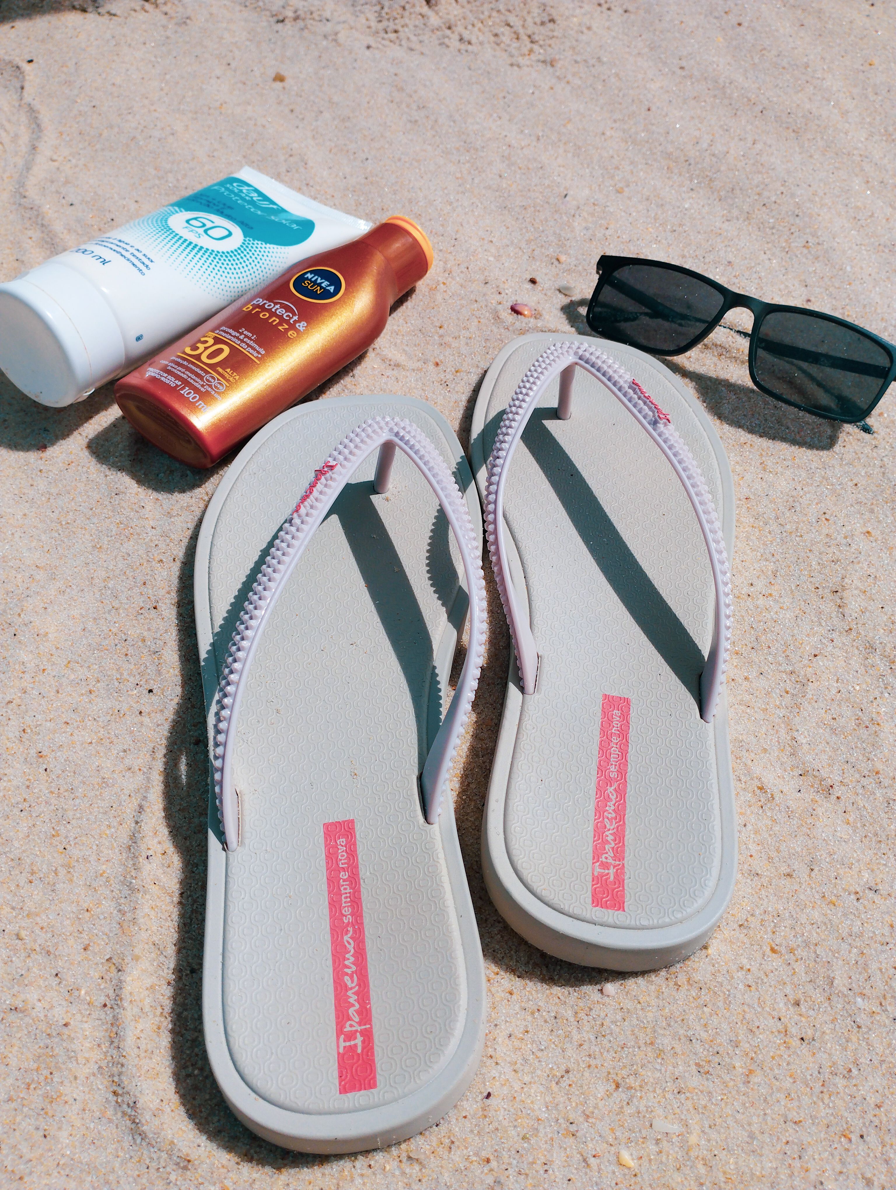 Beach Essentials: Flip-Flops and Sunscreen on Sand · Free Stock Photo