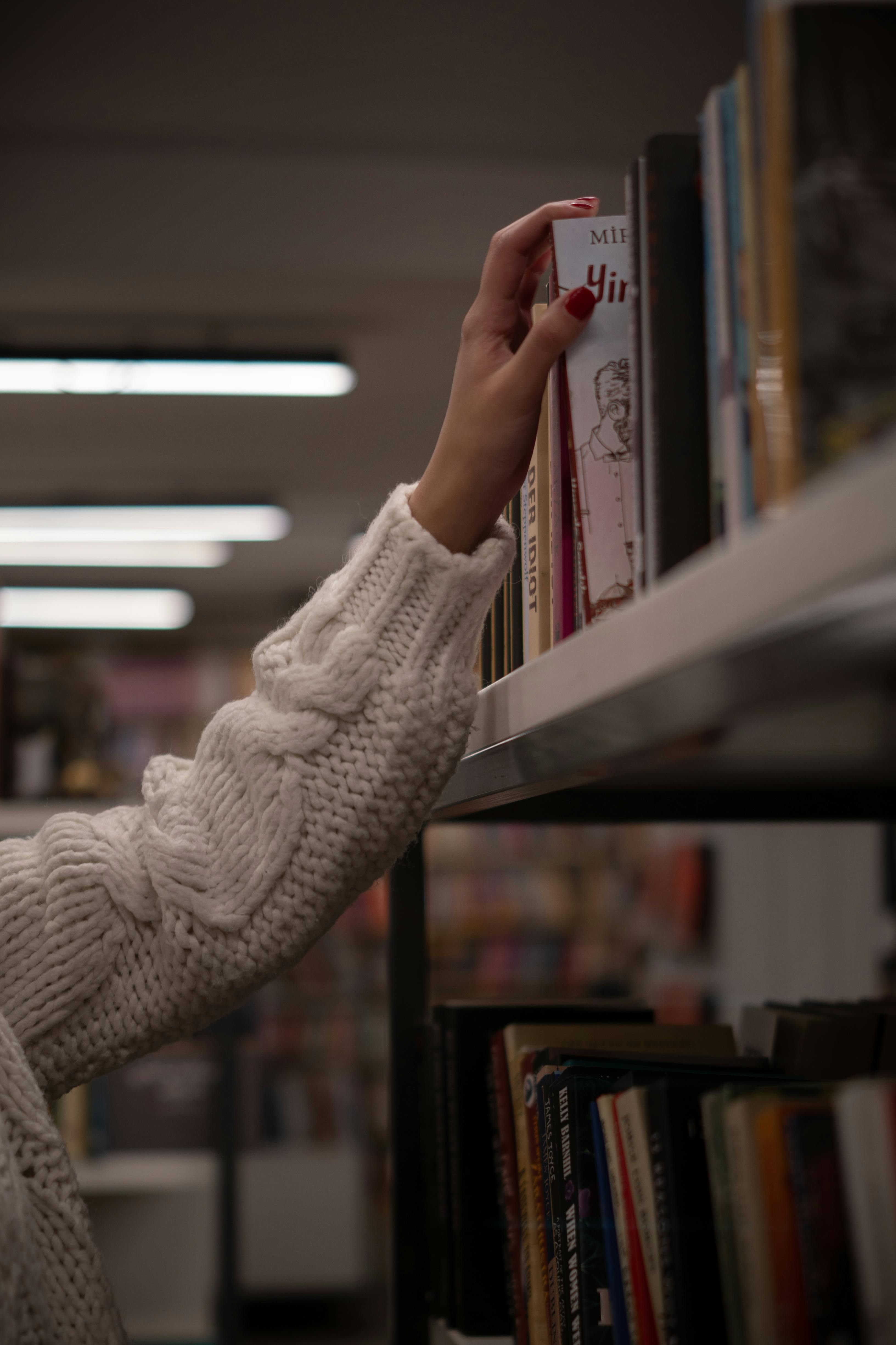 A Close-Up of a Person Reaching for a Book in a Library · Free Stock Photo