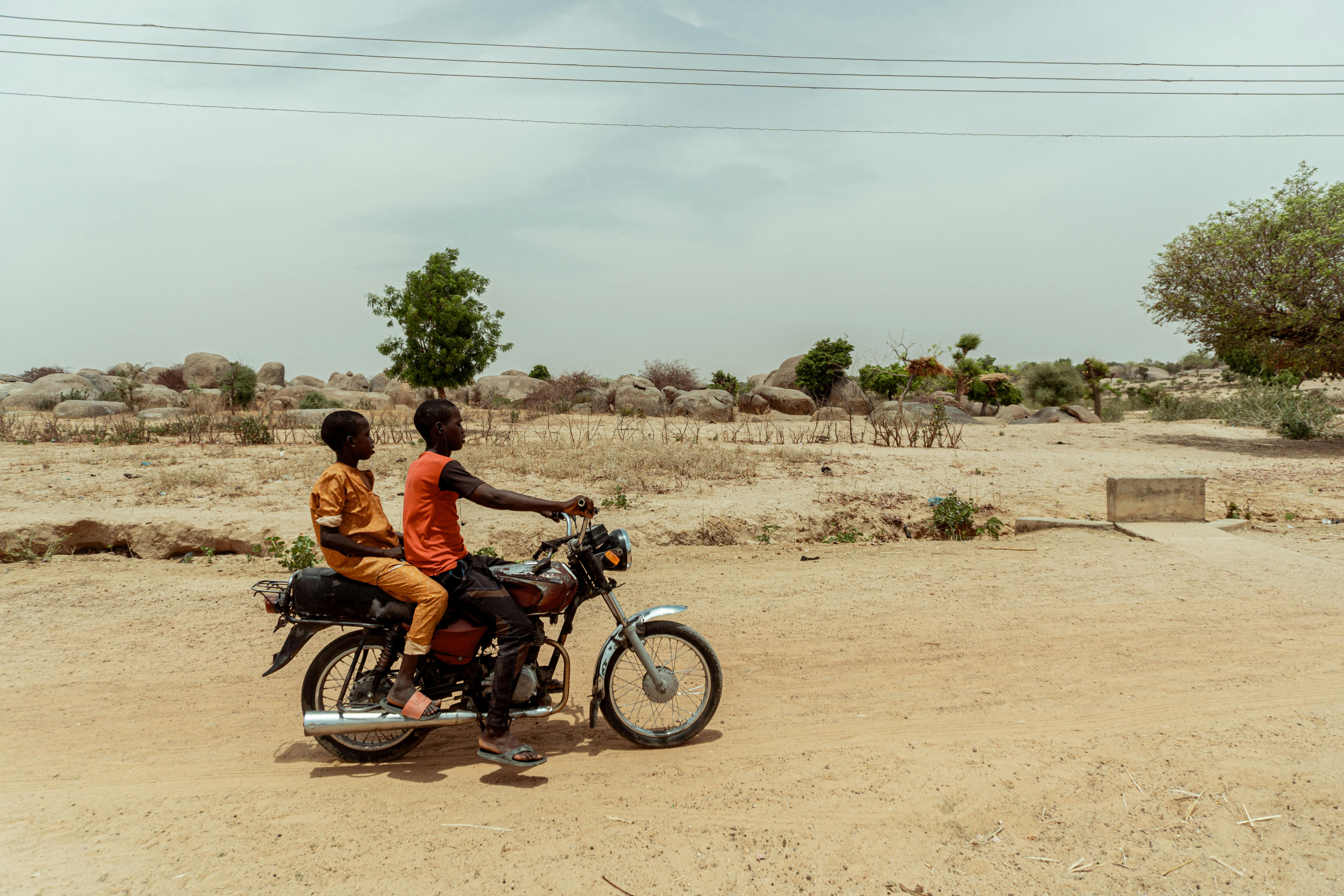 Two people riding motorcycle on dusty road · Free Stock Photo