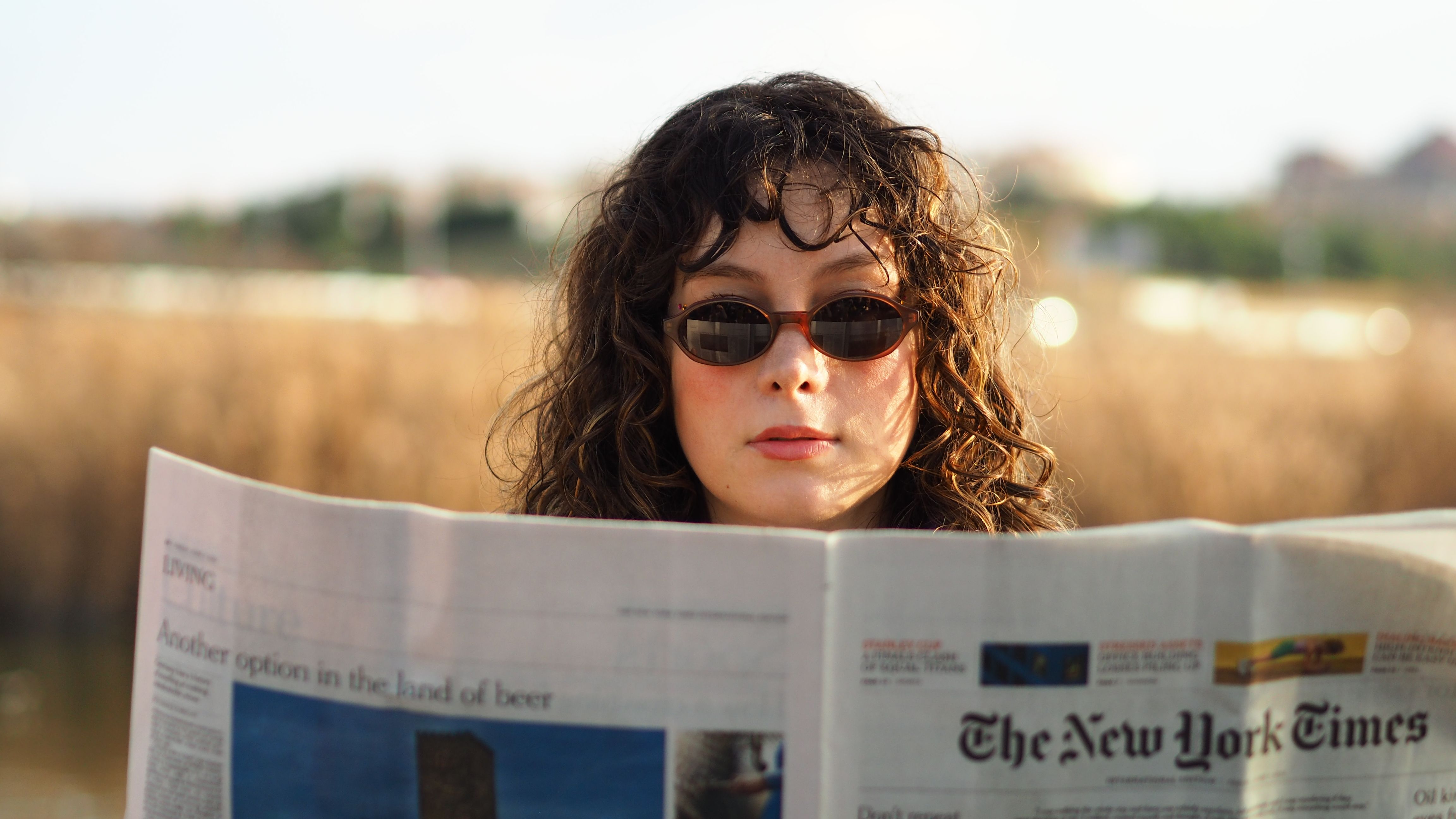 Woman Reading Newspaper Outdoors with Sunglasses · Free Stock Photo