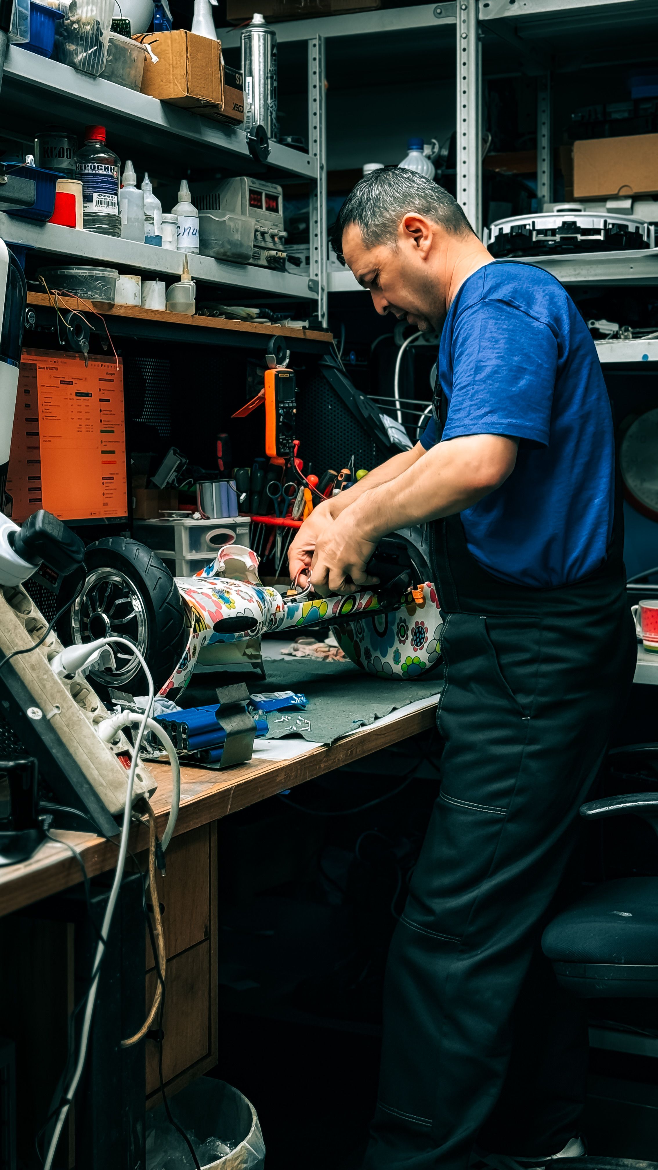 Man Working in Cluttered Workshop Repairing Electronics · Free Stock Photo