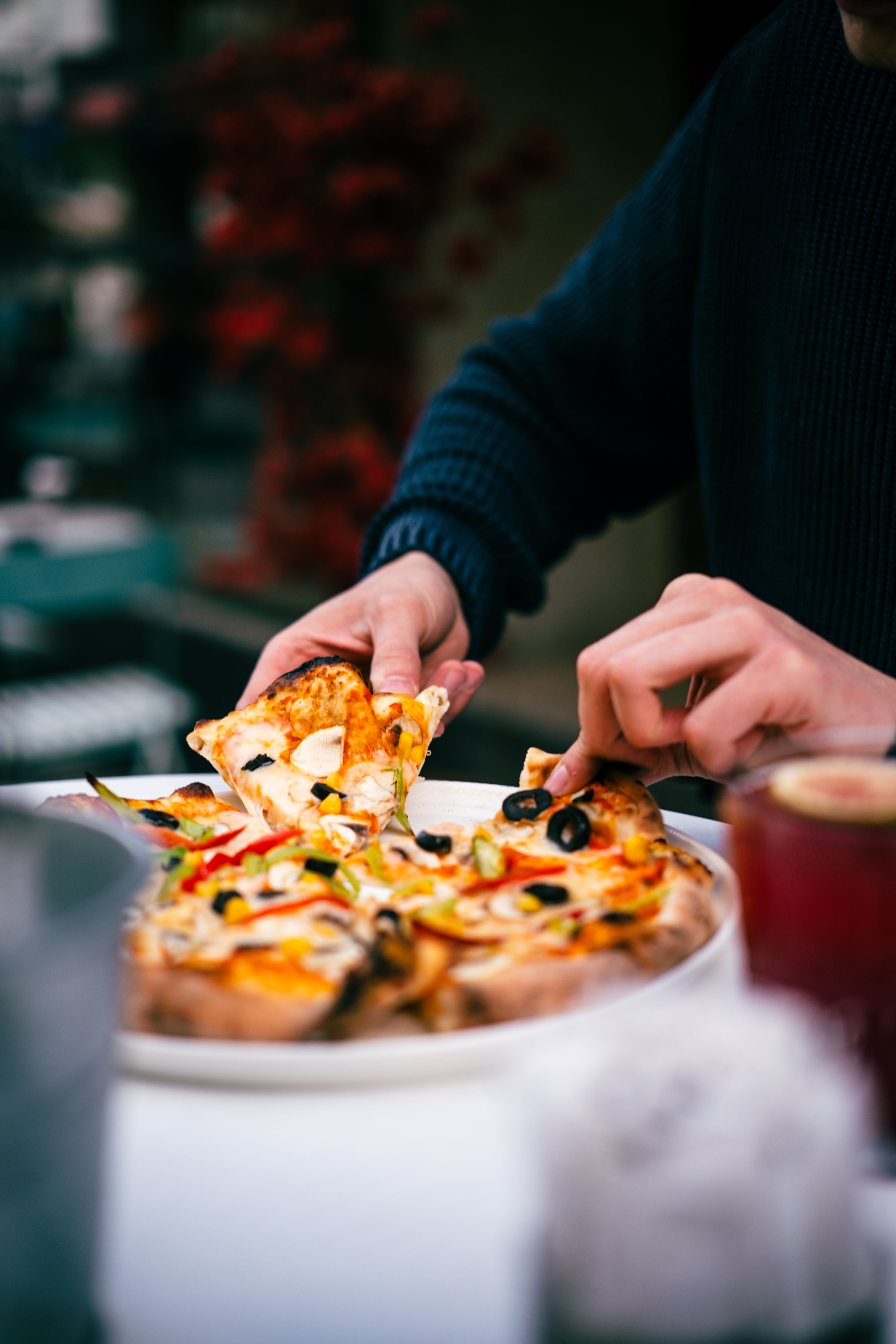 Hand Picking Pizza Slice at Outdoor Cafe · Free Stock Photo